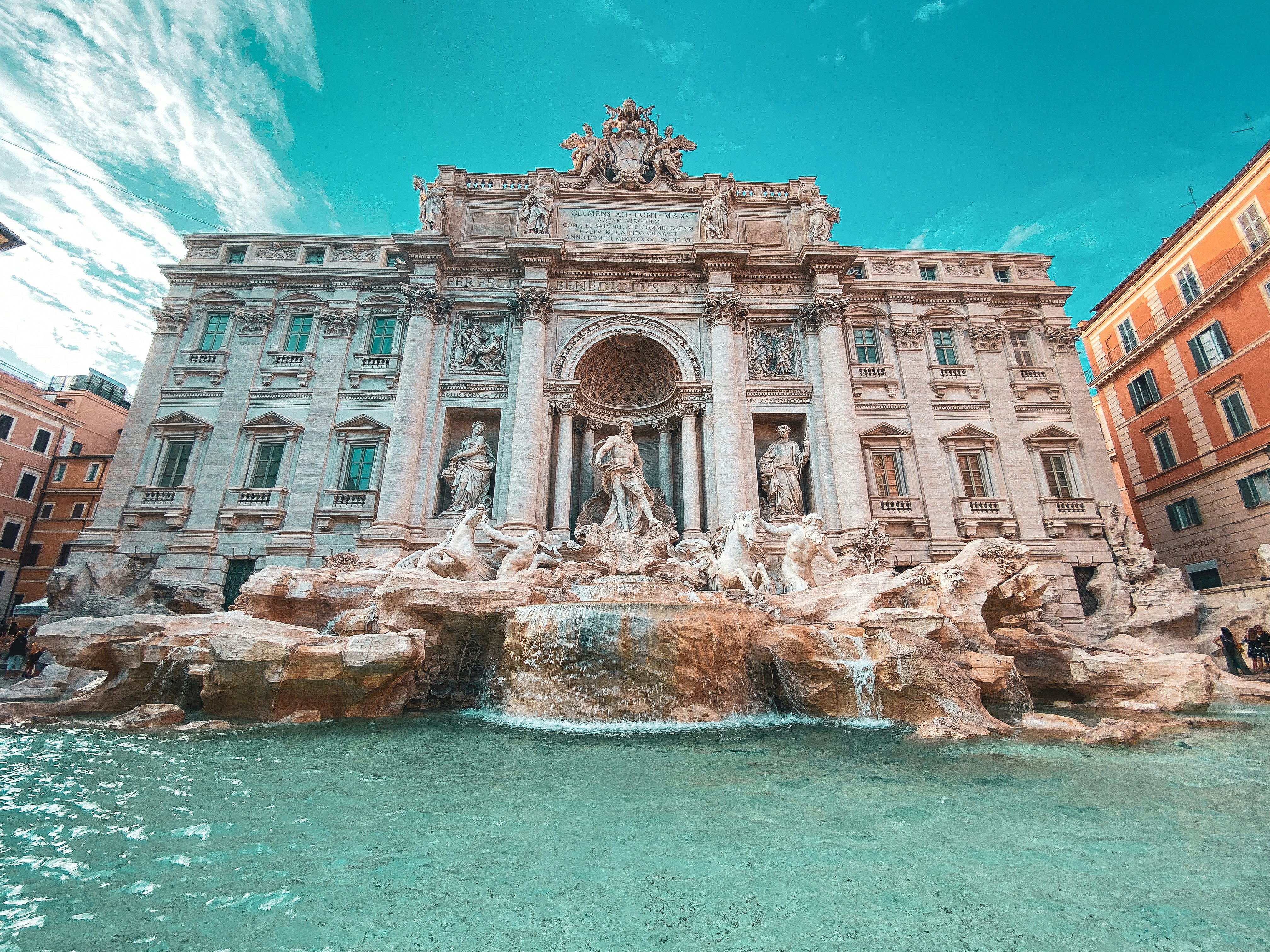 The Trevi Fountain showcases intricate sculptures and flowing waters against a vibrant sky. Visitors admire the historical architecture surrounding the iconic landmark.