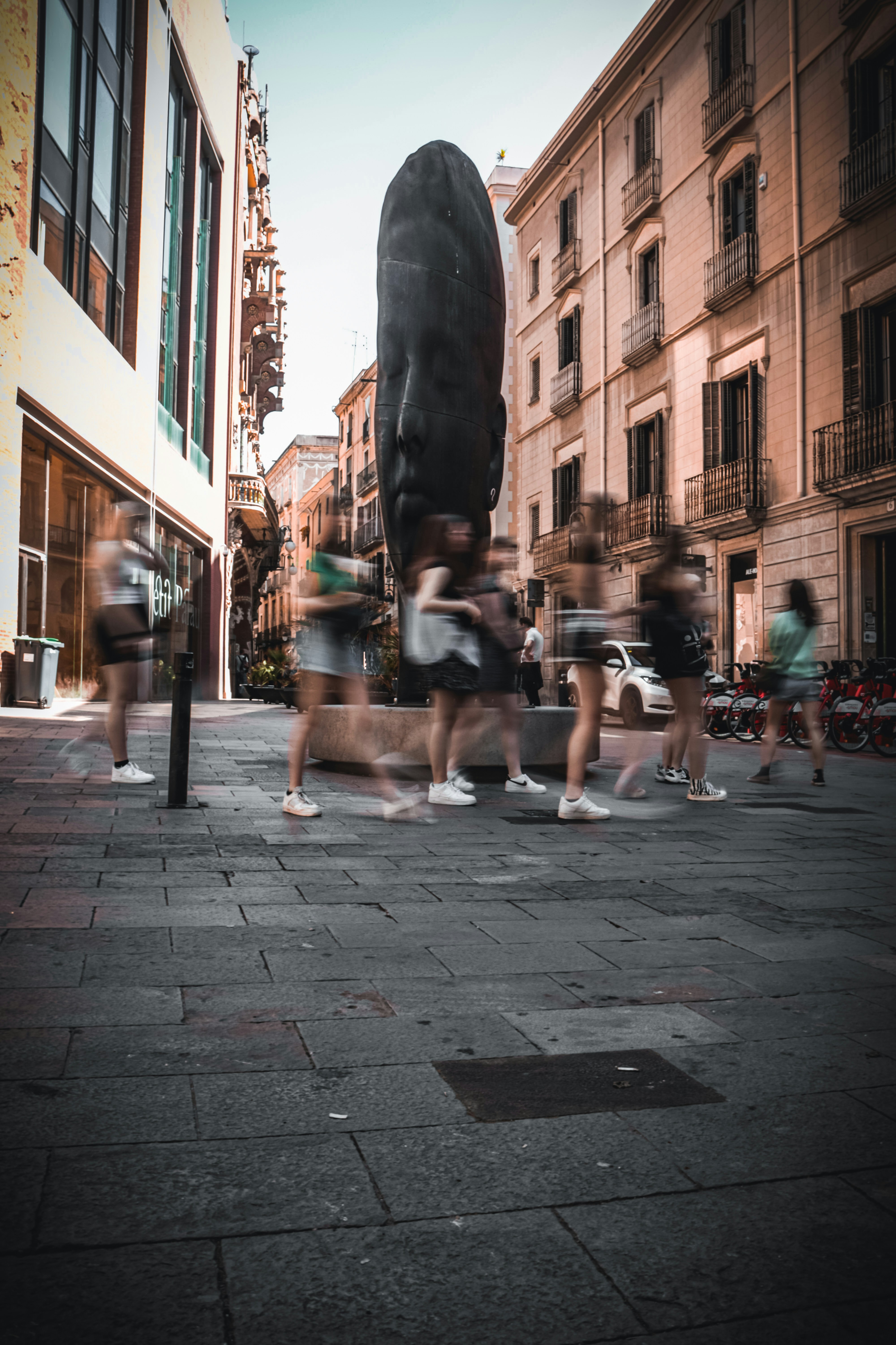 Stride Through Time: A Statue Leads a Blur of People in a City Bloc
