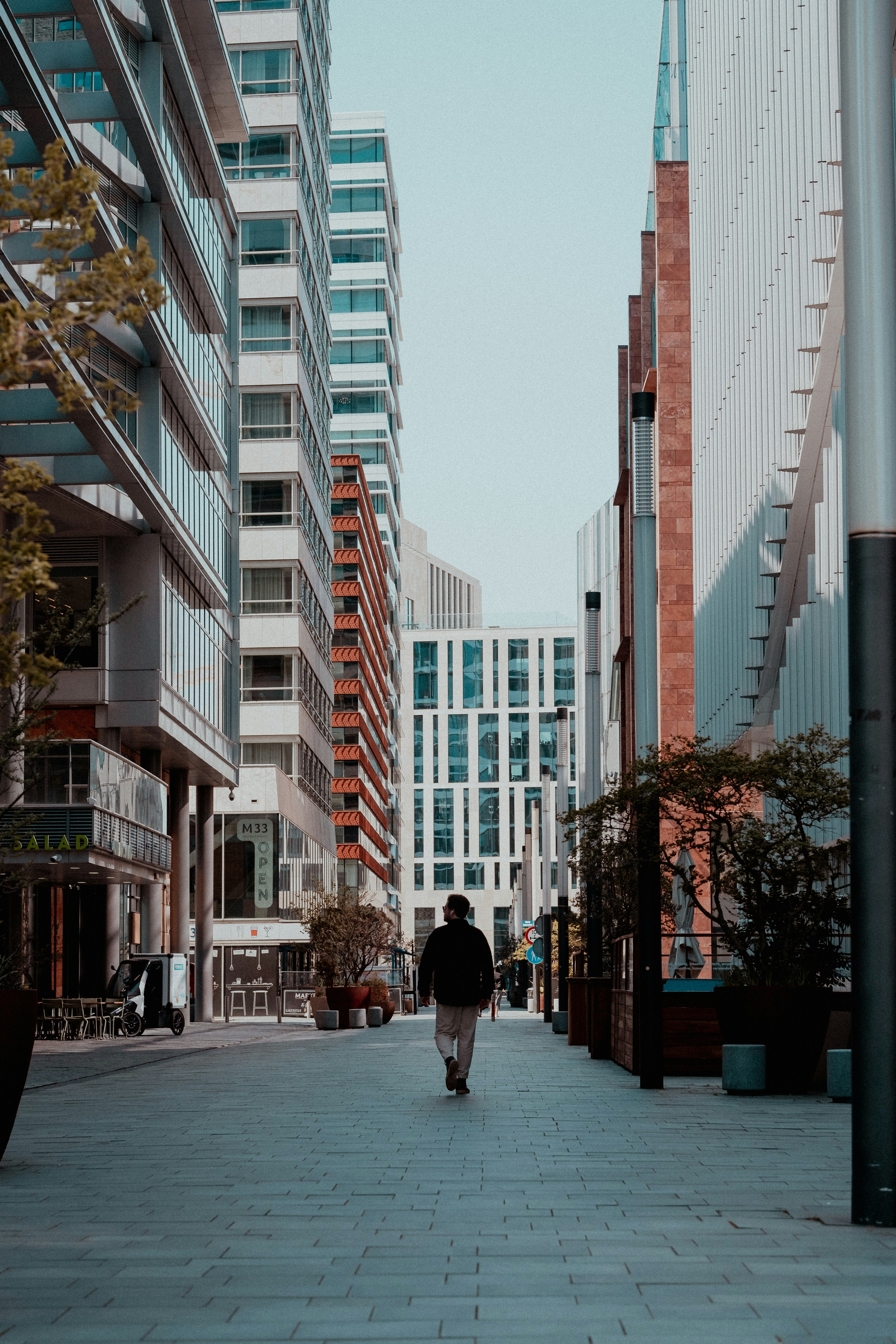 A person walking on a street between tall buildings photo – Free ...