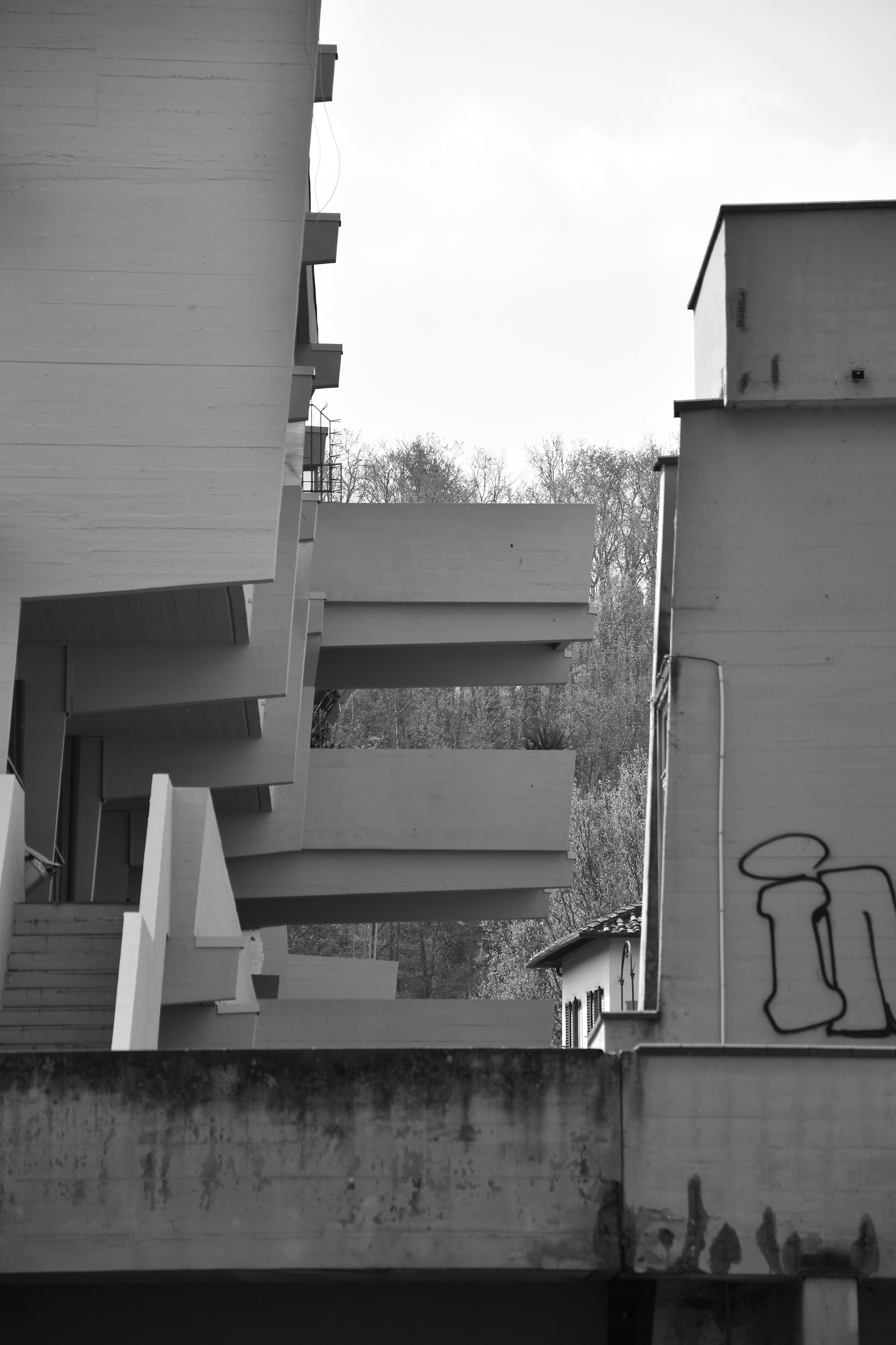 Abstract view of layered architectural structures with a hint of nature in the background. The composition emphasizes geometric forms and contrasts.