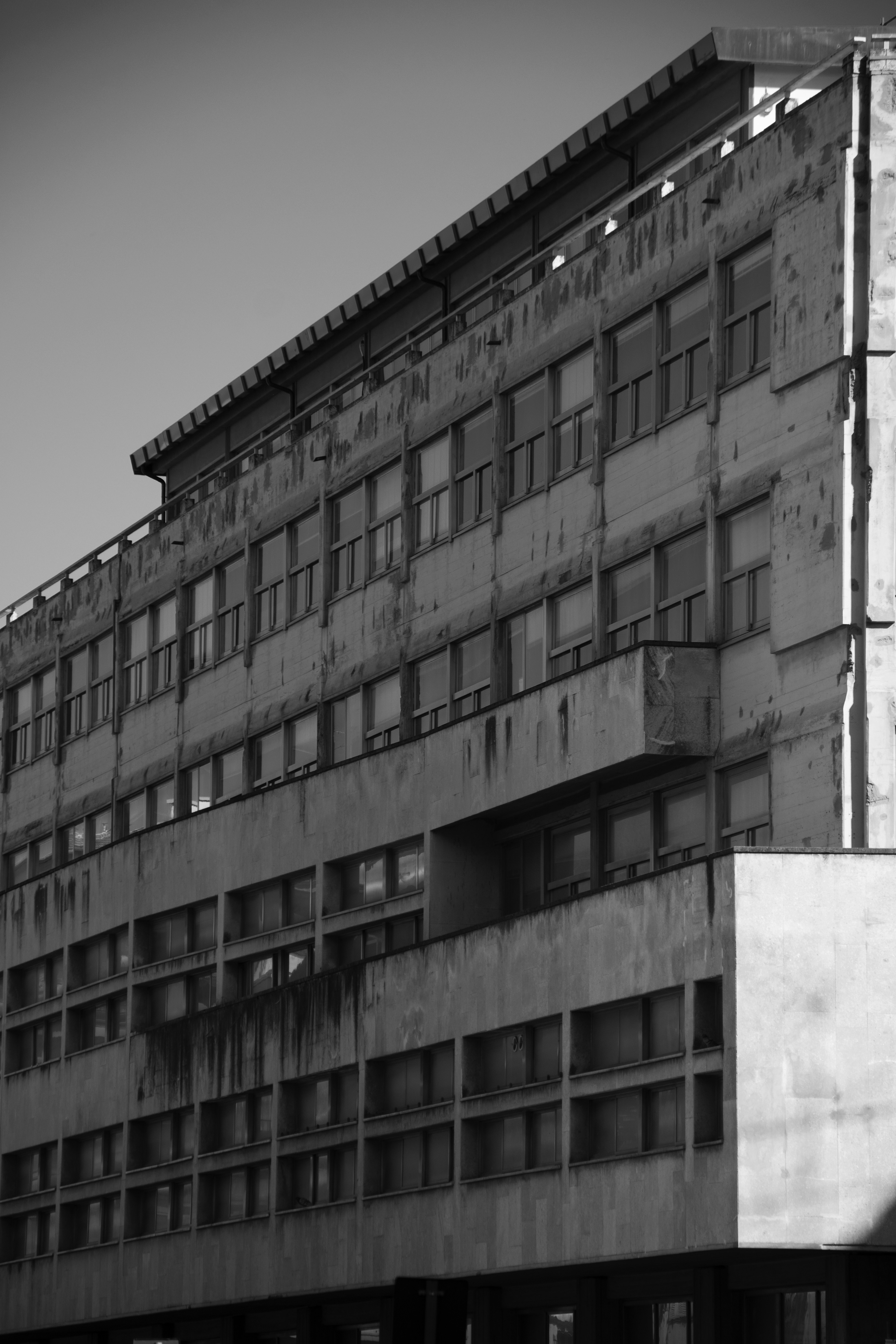 Weathered concrete building with a stark facade and numerous windows, showcasing signs of age and neglect.