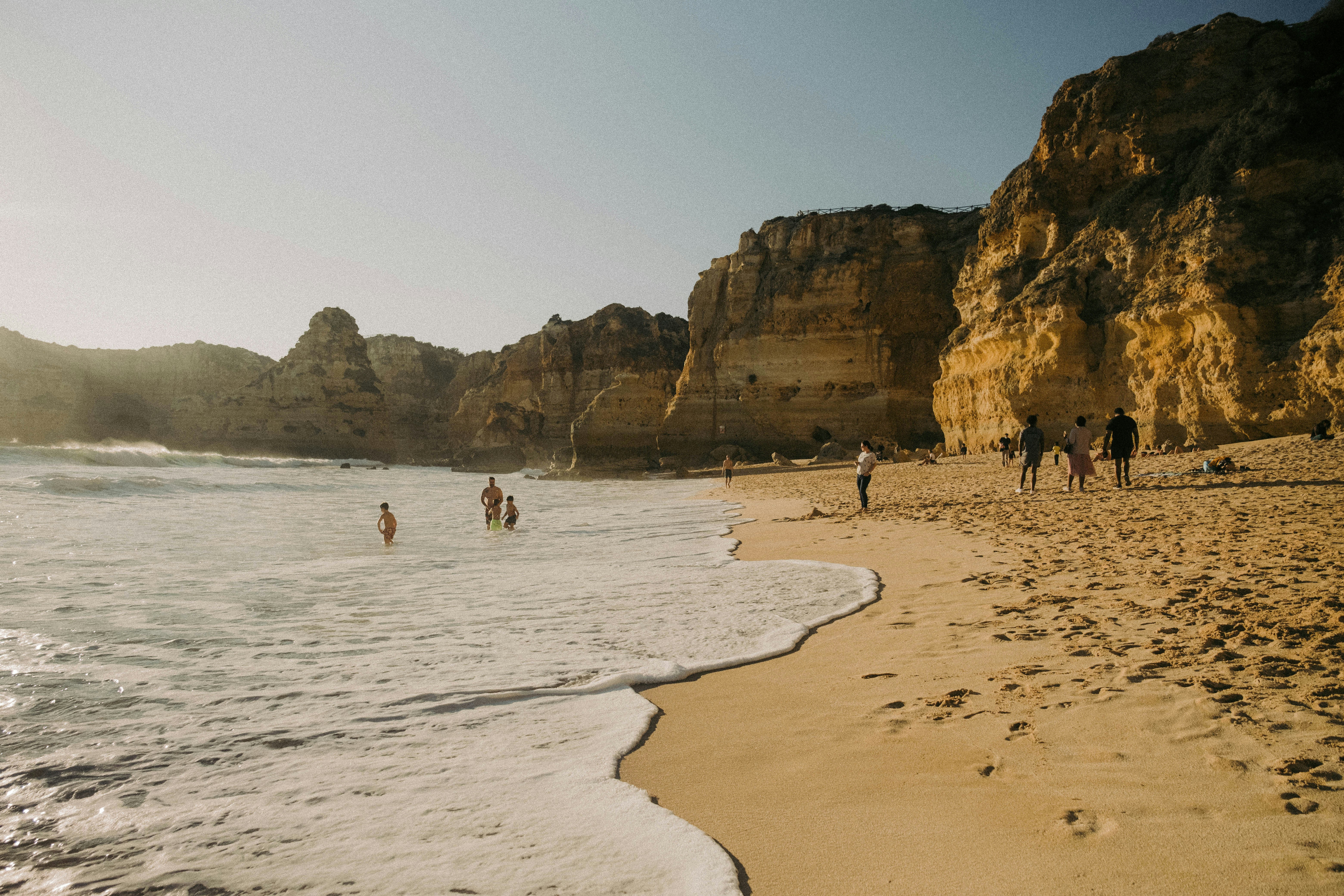 People enjoying the serene beach with golden cliffs under a clear sky.
