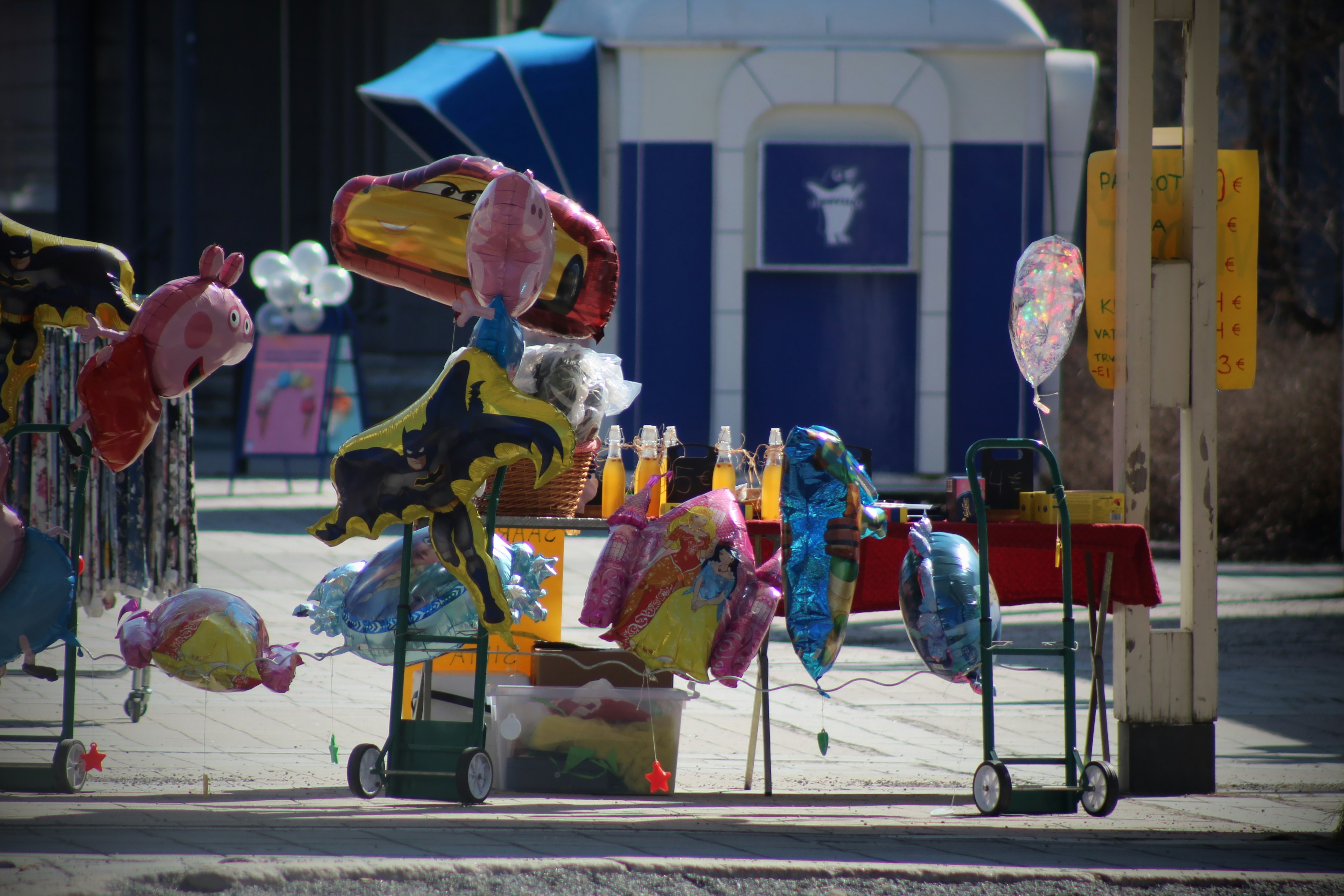 Colorful assortment of balloons attached to carts on a sunlit street.