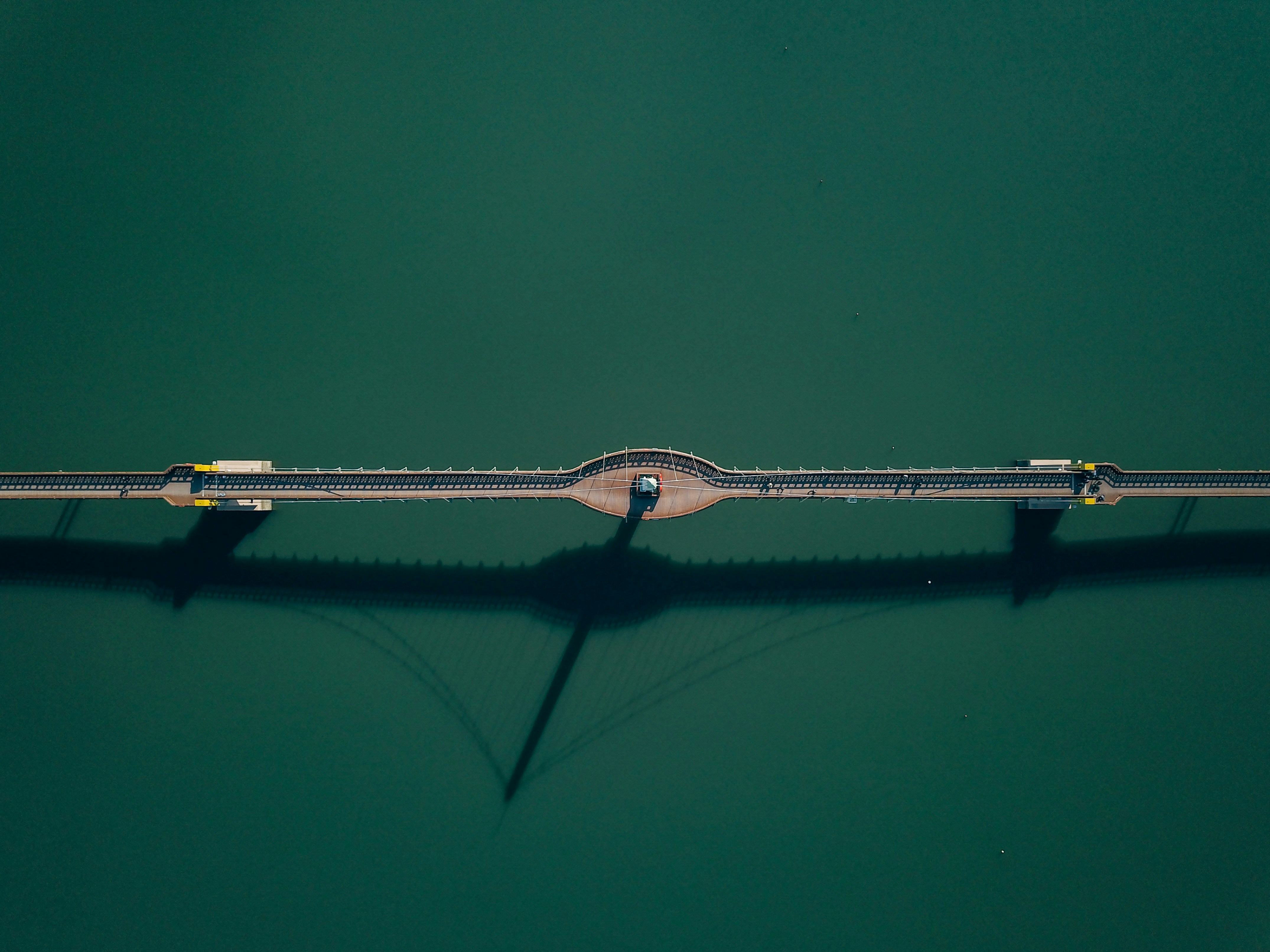 Aerial Span: Central Bridge Pier Casting Line Shadows on Calm Green Water