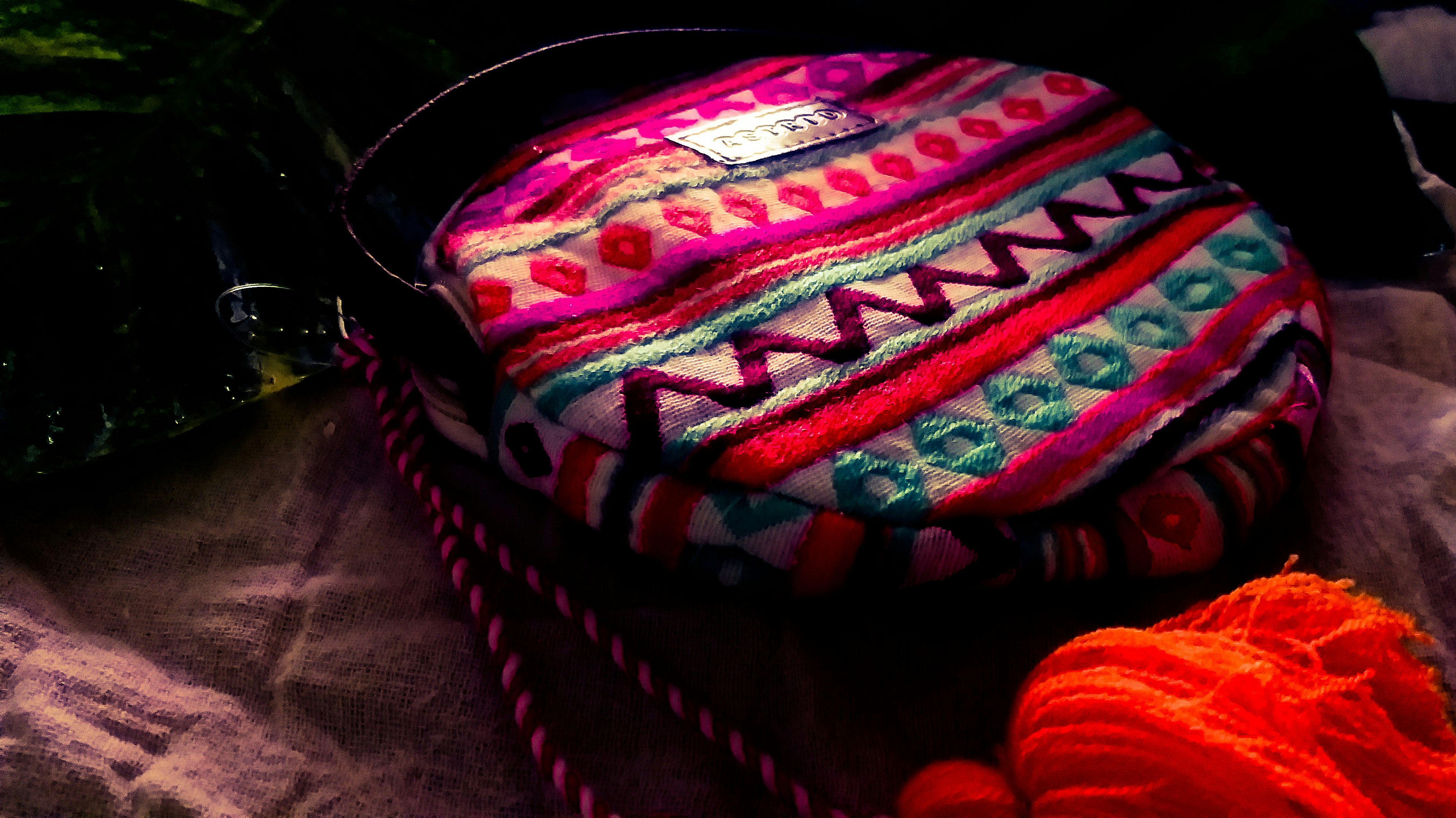 Colorful round bag adorned with intricate patterns and a bright tassel, resting on a textured surface.
