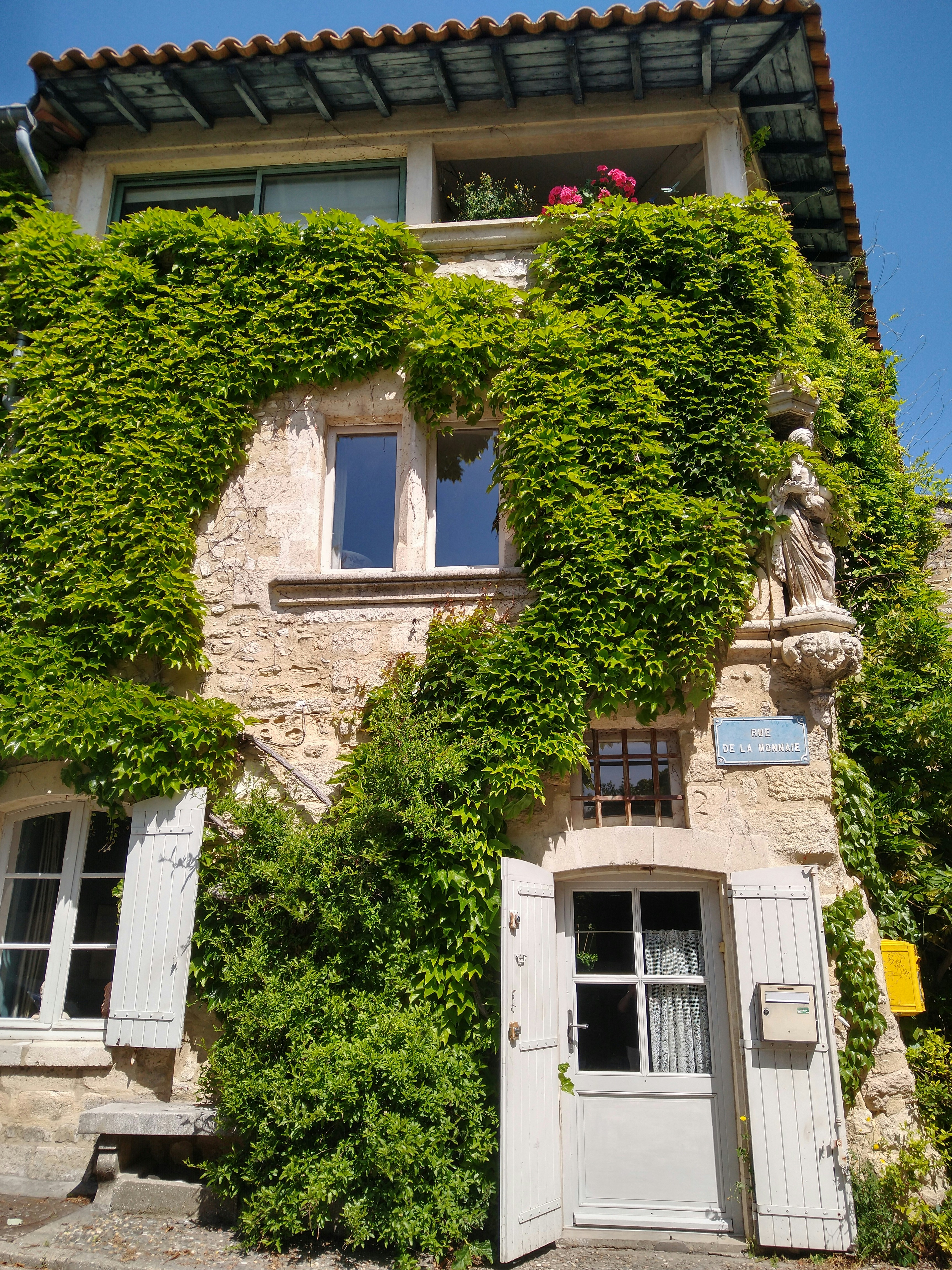 Stone house with ivy-covered facade and open shutters under a clear blue sky.