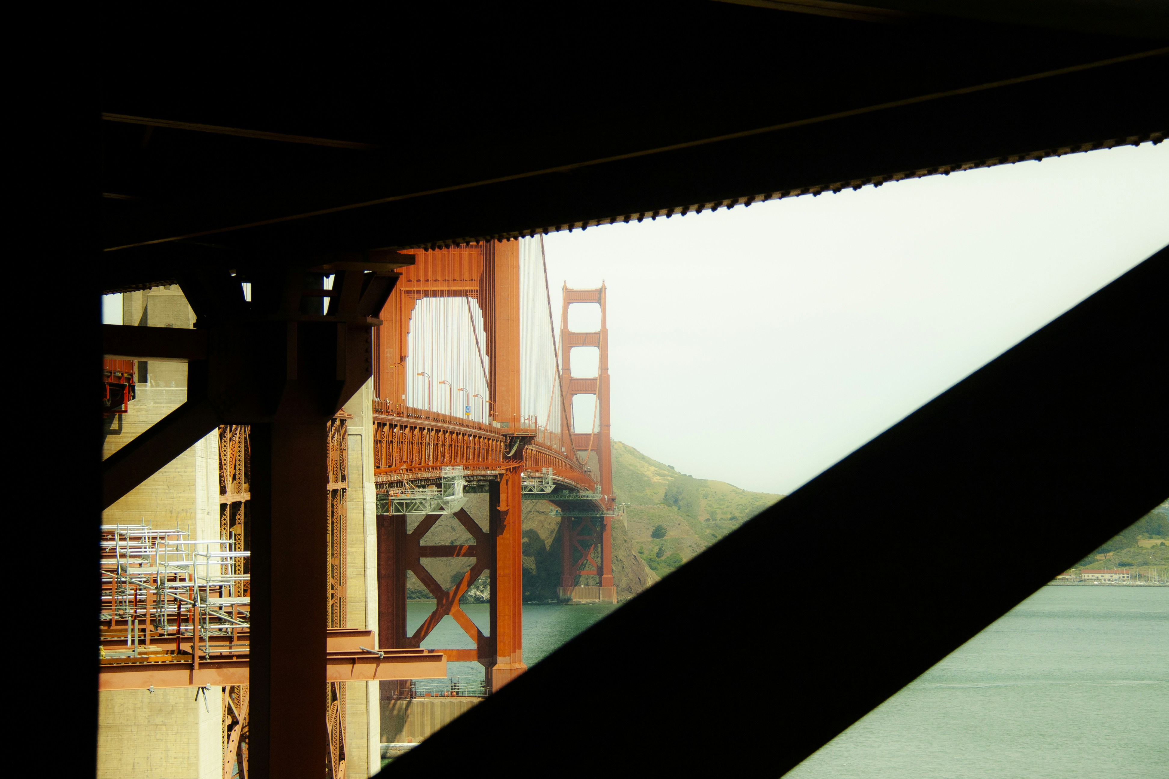 Golden Gate Bridge viewed through structural beams, showcasing intricate designs against a serene bay backdrop.