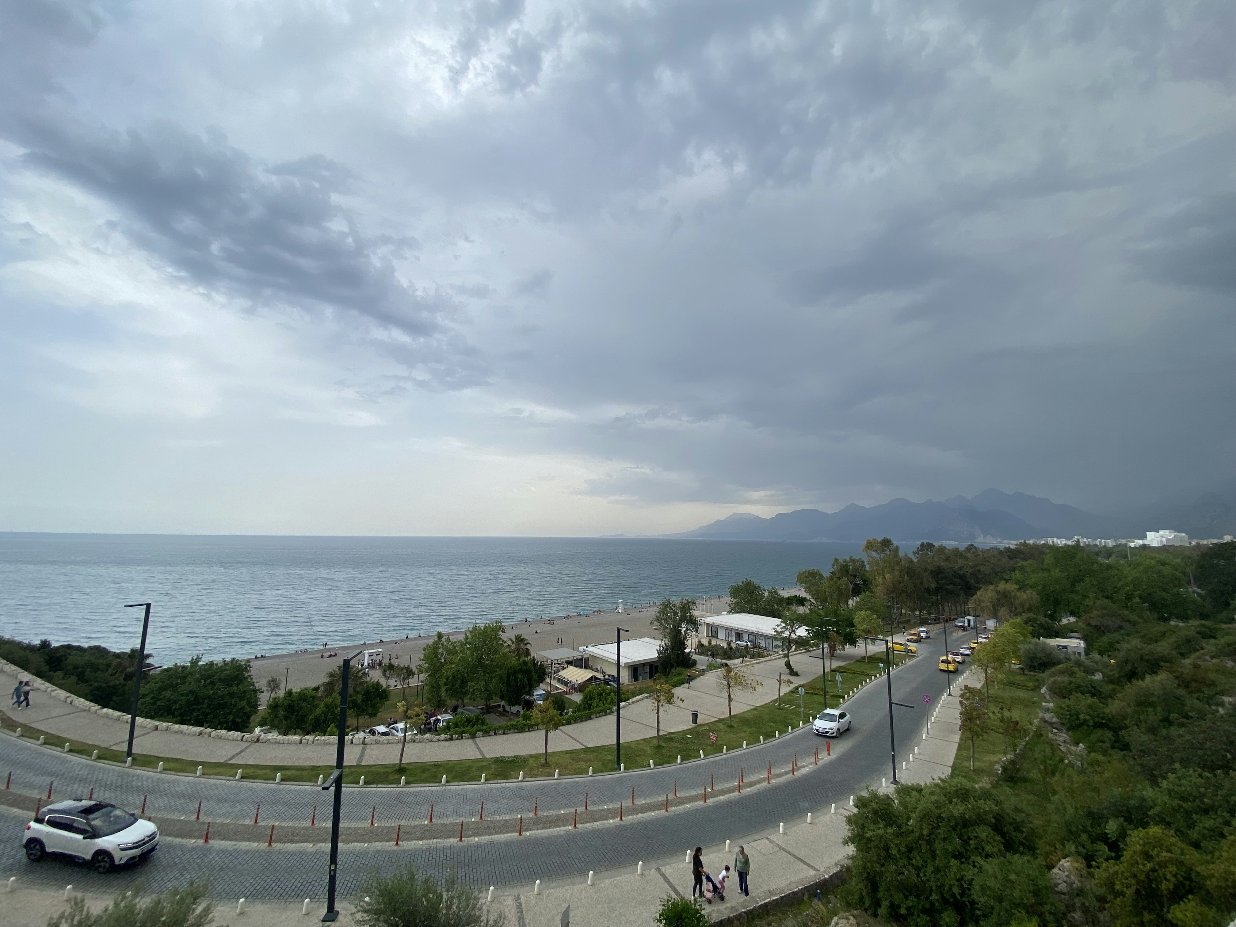 Dramatic seascape with dark clouds looming over a tranquil beach, where a winding road leads to the horizon. The scene captures a moment before the storm.