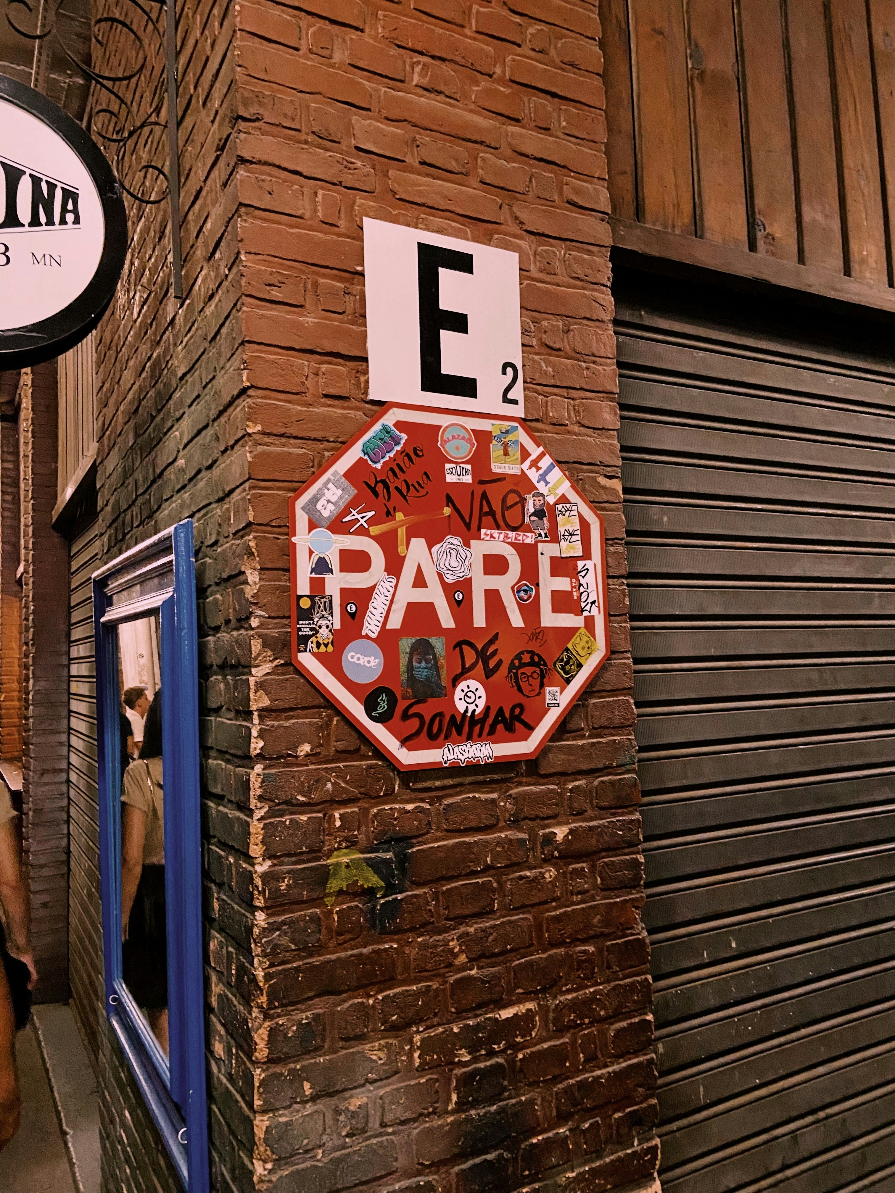 Stickered octagonal sign on a brick corner beside a blue-framed window