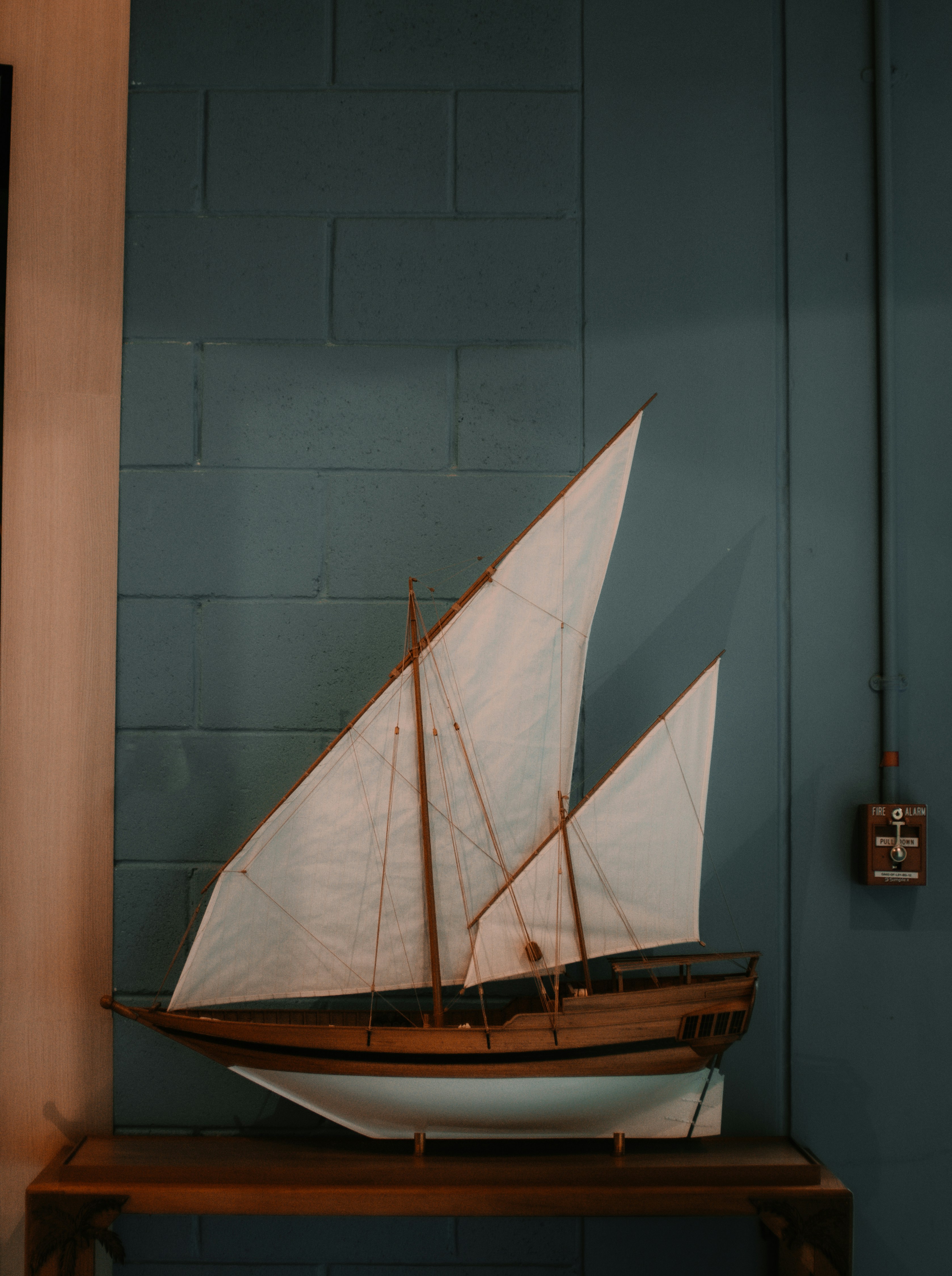Intricately crafted model sailboat displayed against a textured blue wall, showcasing fine details of the sails and hull. 