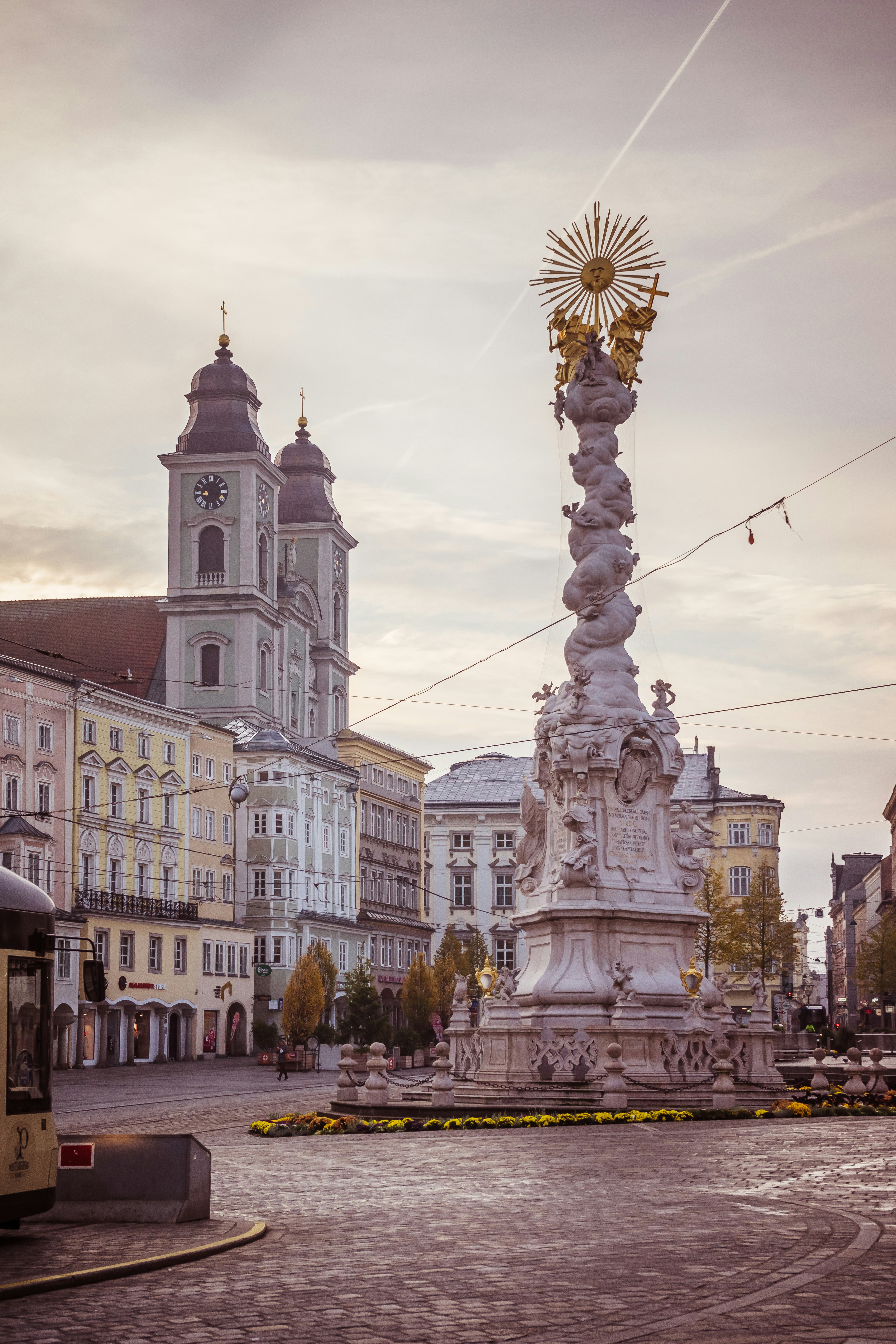 Intricate Baroque fountain adorned with golden sunburst, set against a backdrop of historic architecture in a vibrant town square.
