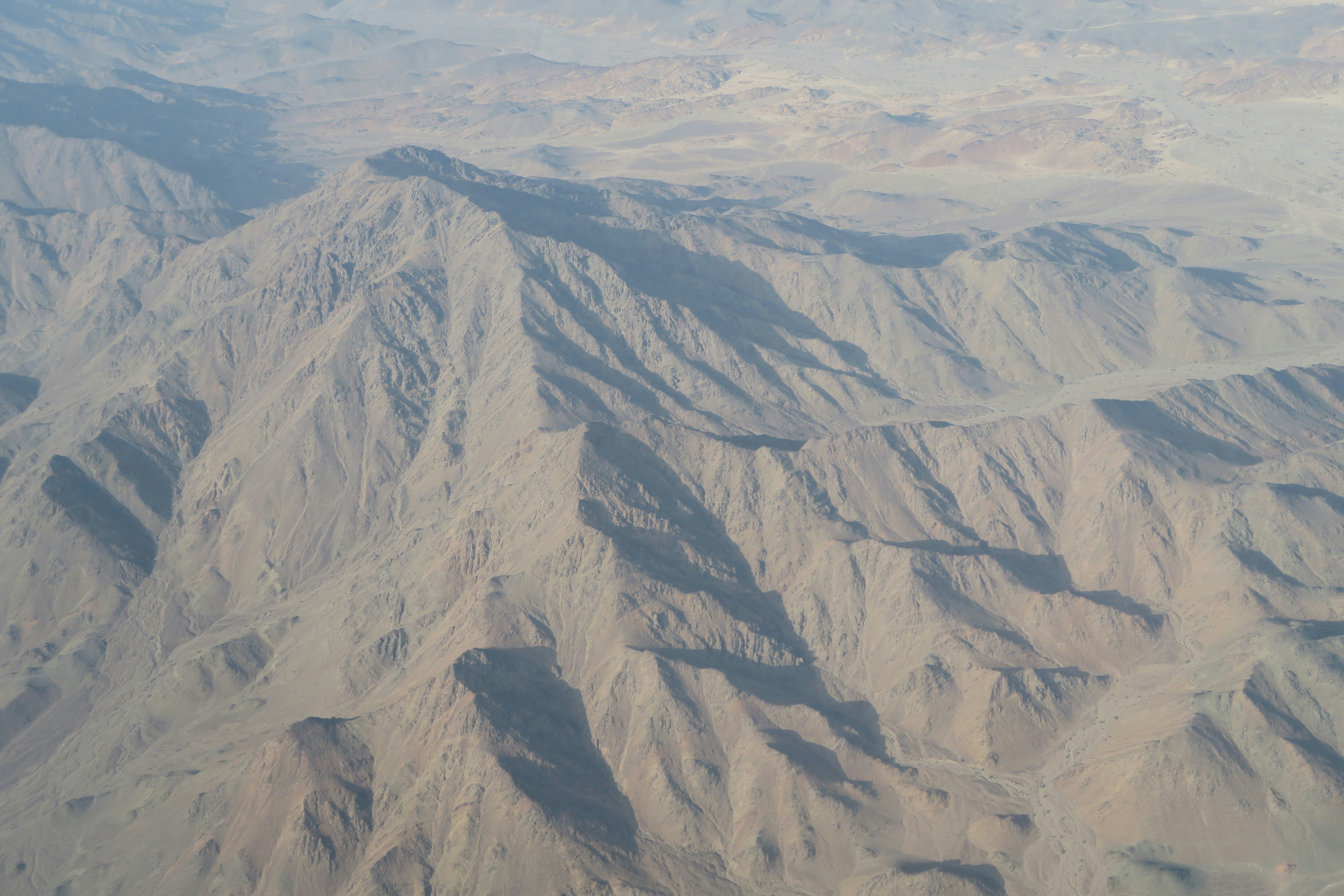Aerial view of rugged mountain ranges showcasing intricate geological formations and shadows cast by the sun.
