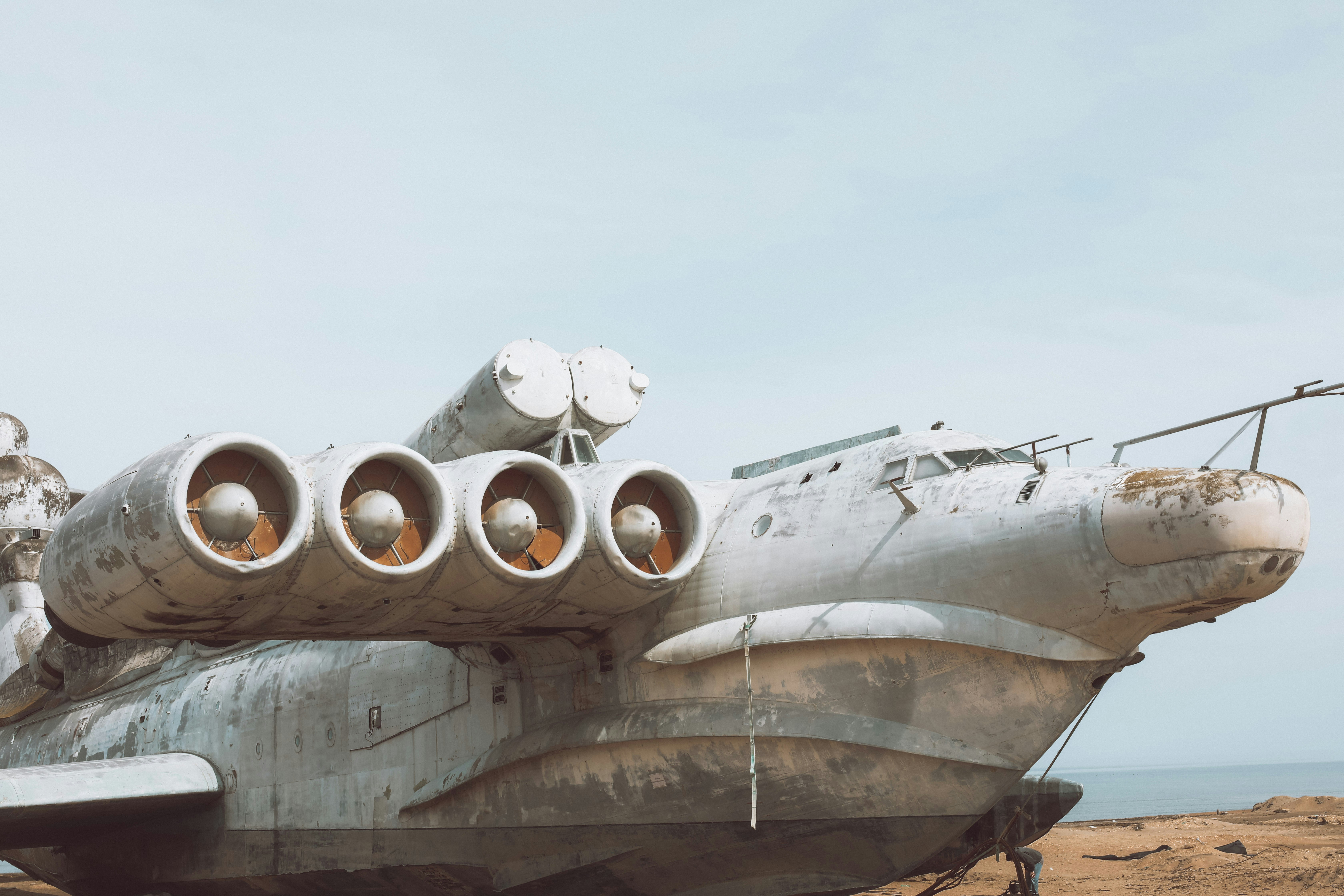 Soviet ekranoplan with multiple jet engines rests on sandy shore under a clear sky.