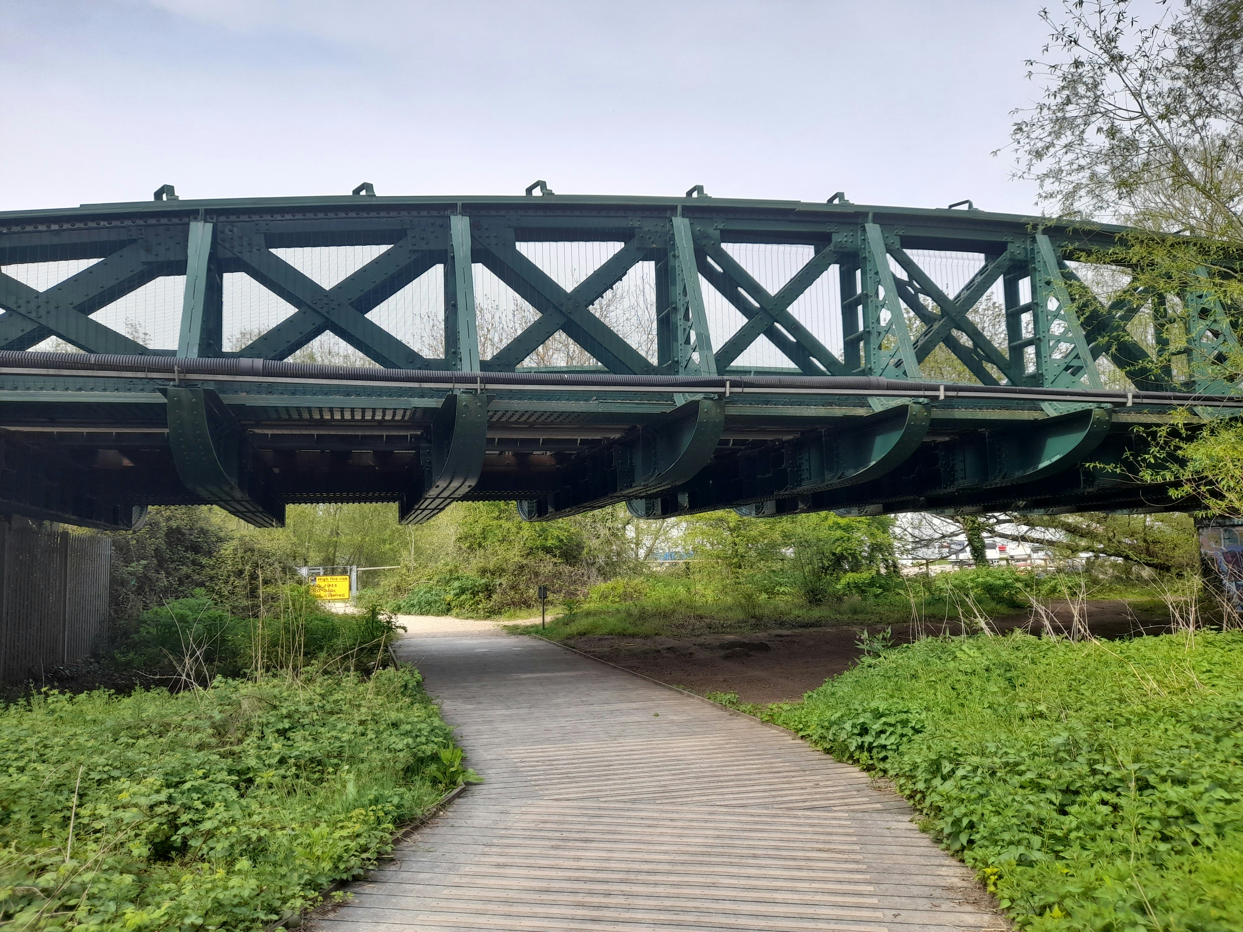 An arched steel railway bridge close to footpath, you can stand right underneath and watch the train speed above you. I love the strength of the ironwork and the beauty of the design. It is thrilling when you stand beneath the ironwork and you see the train pulse above you.
