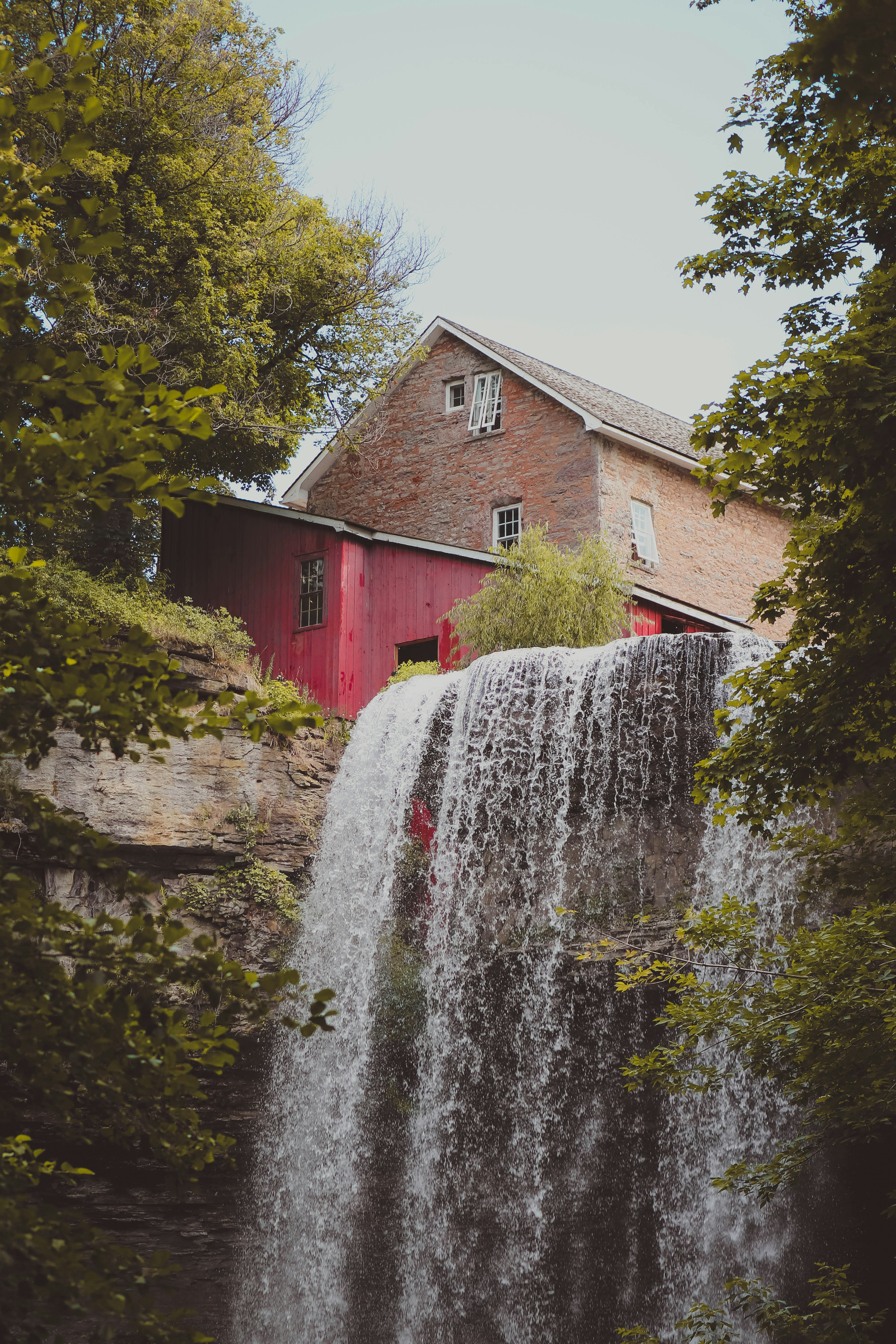 Red Mill at the Edge: Waterfall Curtain Beneath a Rustic Crest