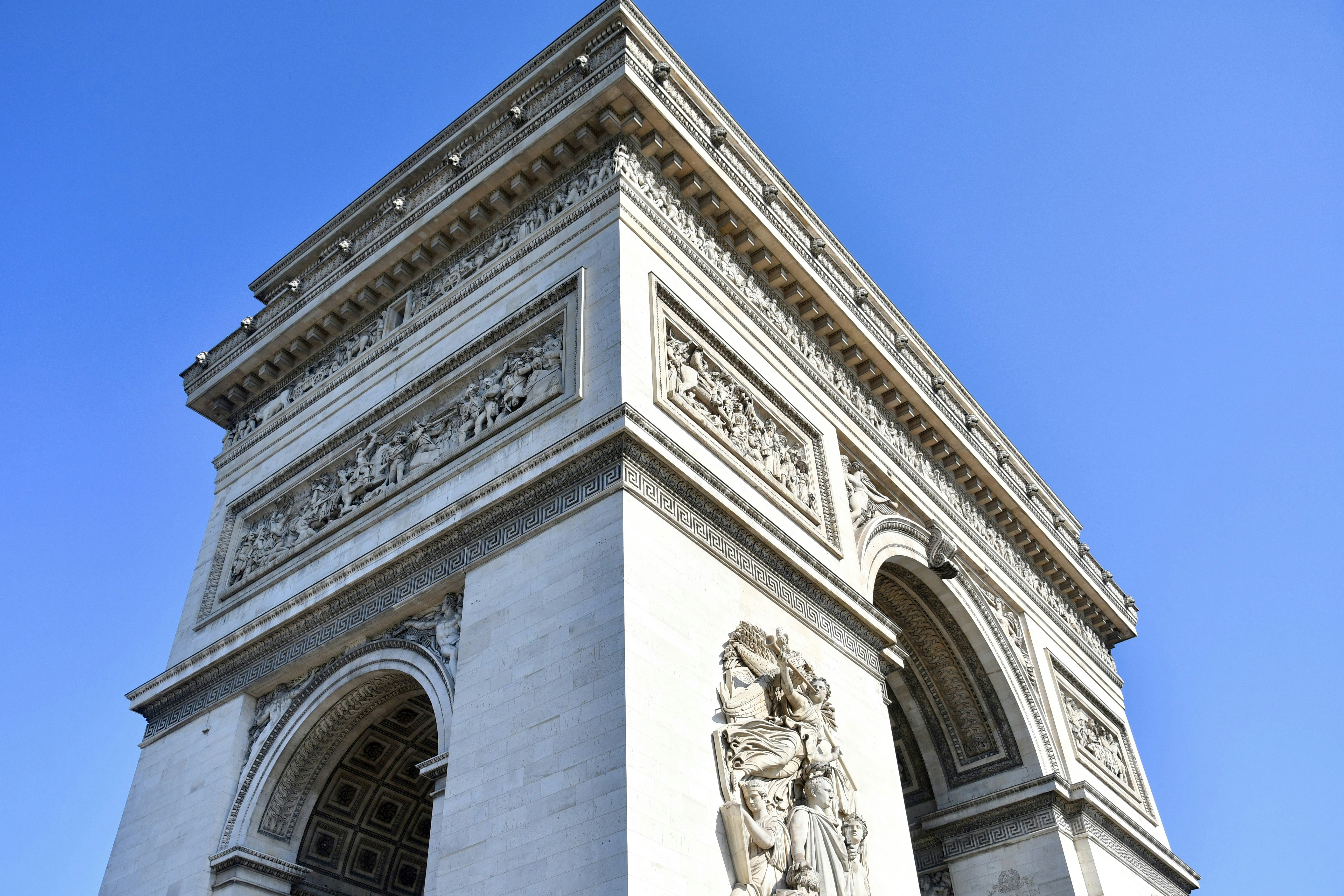 Cornered Triumph: Carved Relief on a Stone Arch Against a Clear Blue Sky
