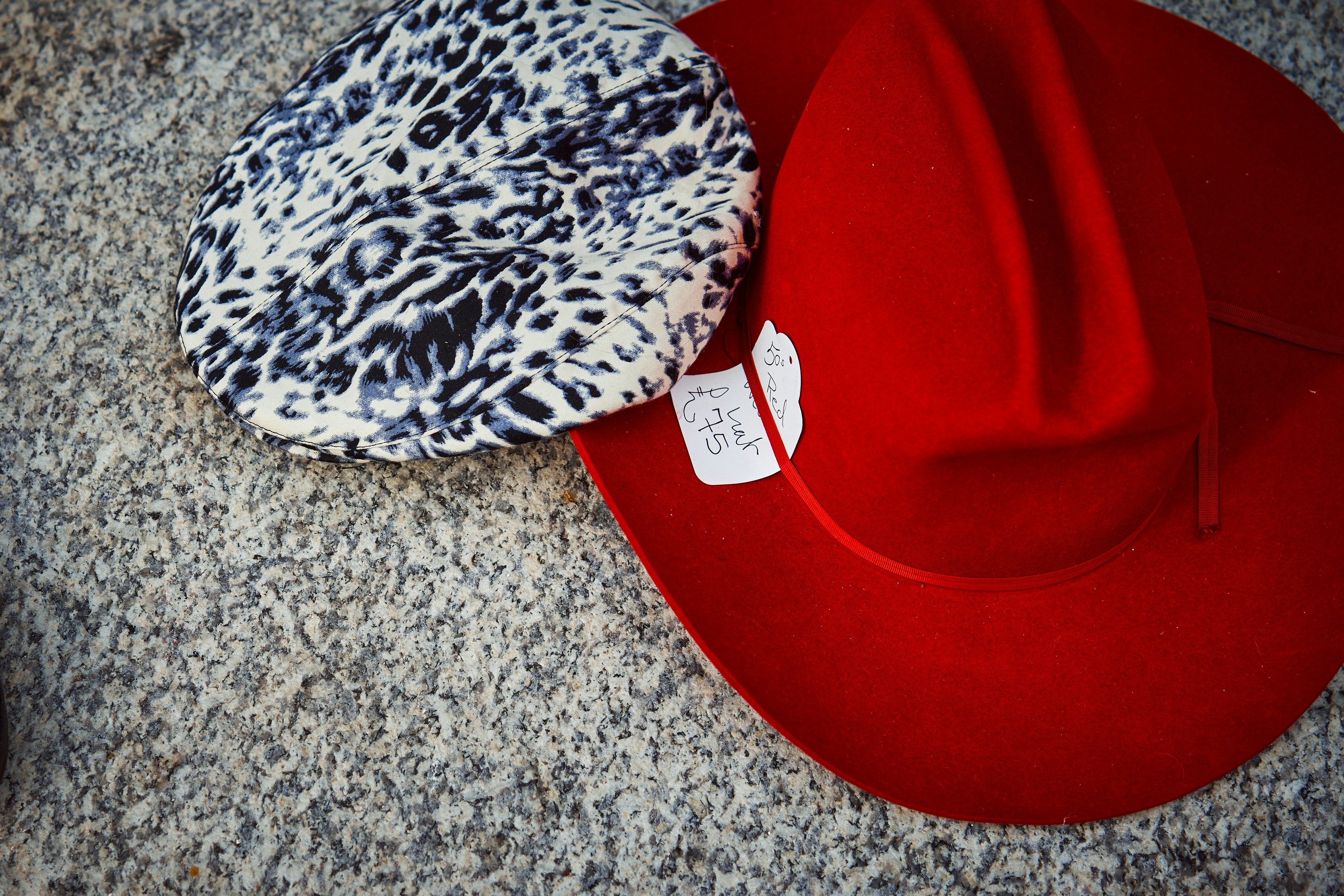 A vibrant red cowboy hat rests alongside a patterned black-and-white cap on a textured surface.