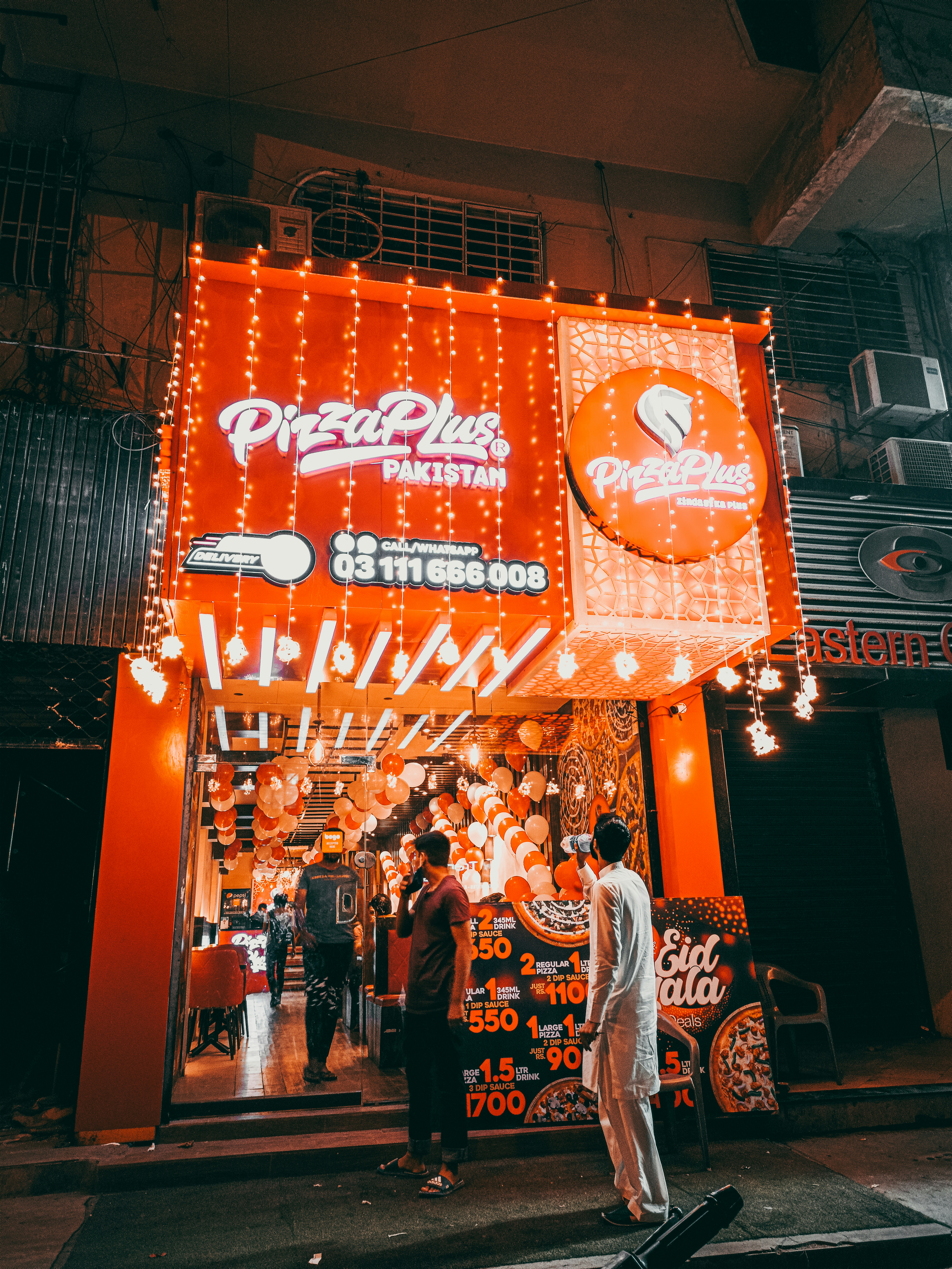 Vibrant storefront of PizzaPlus adorned with colorful lights and festive decorations, inviting customers in for a delicious meal.