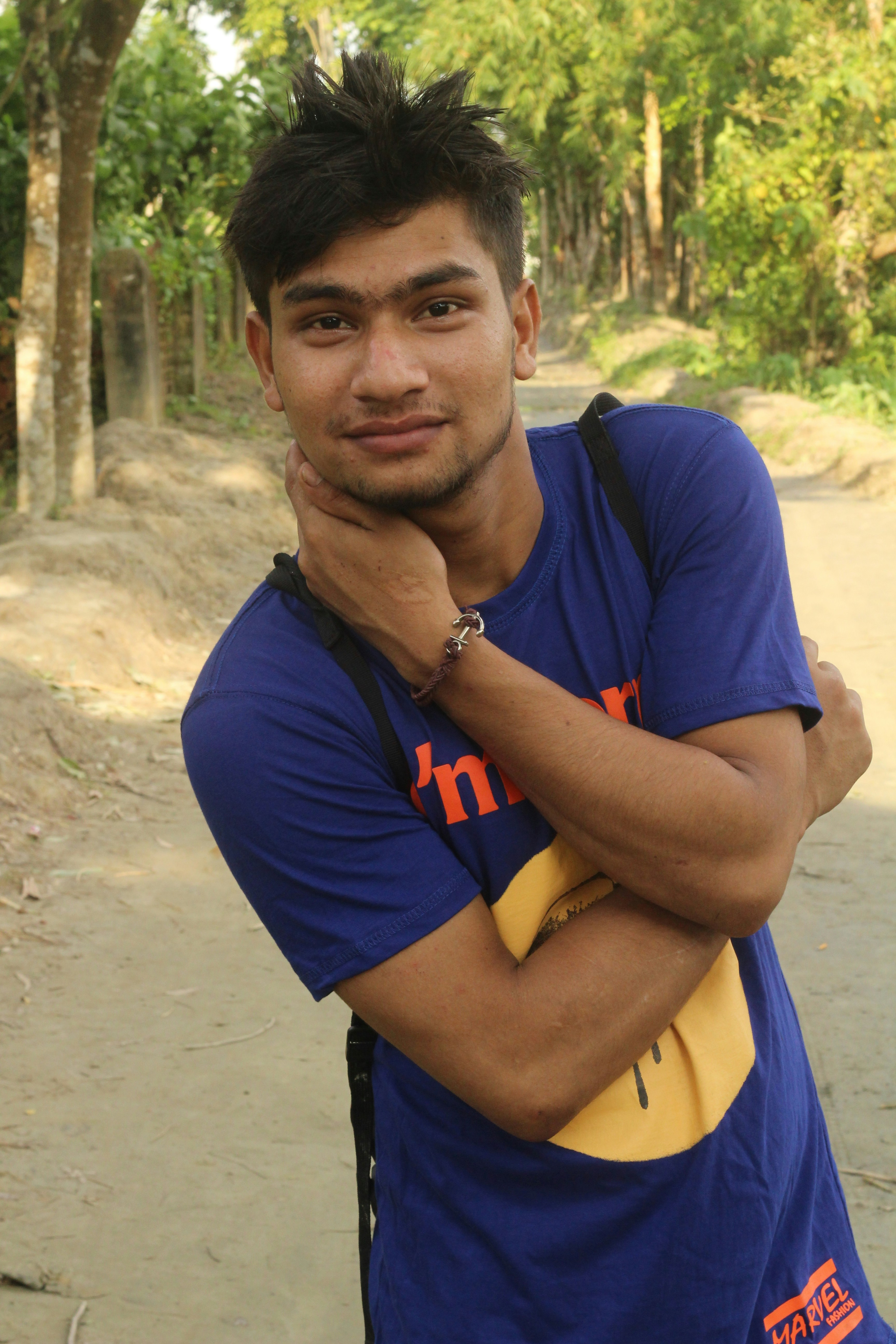 Young man posing thoughtfully on a tranquil dirt path surrounded by greenery.