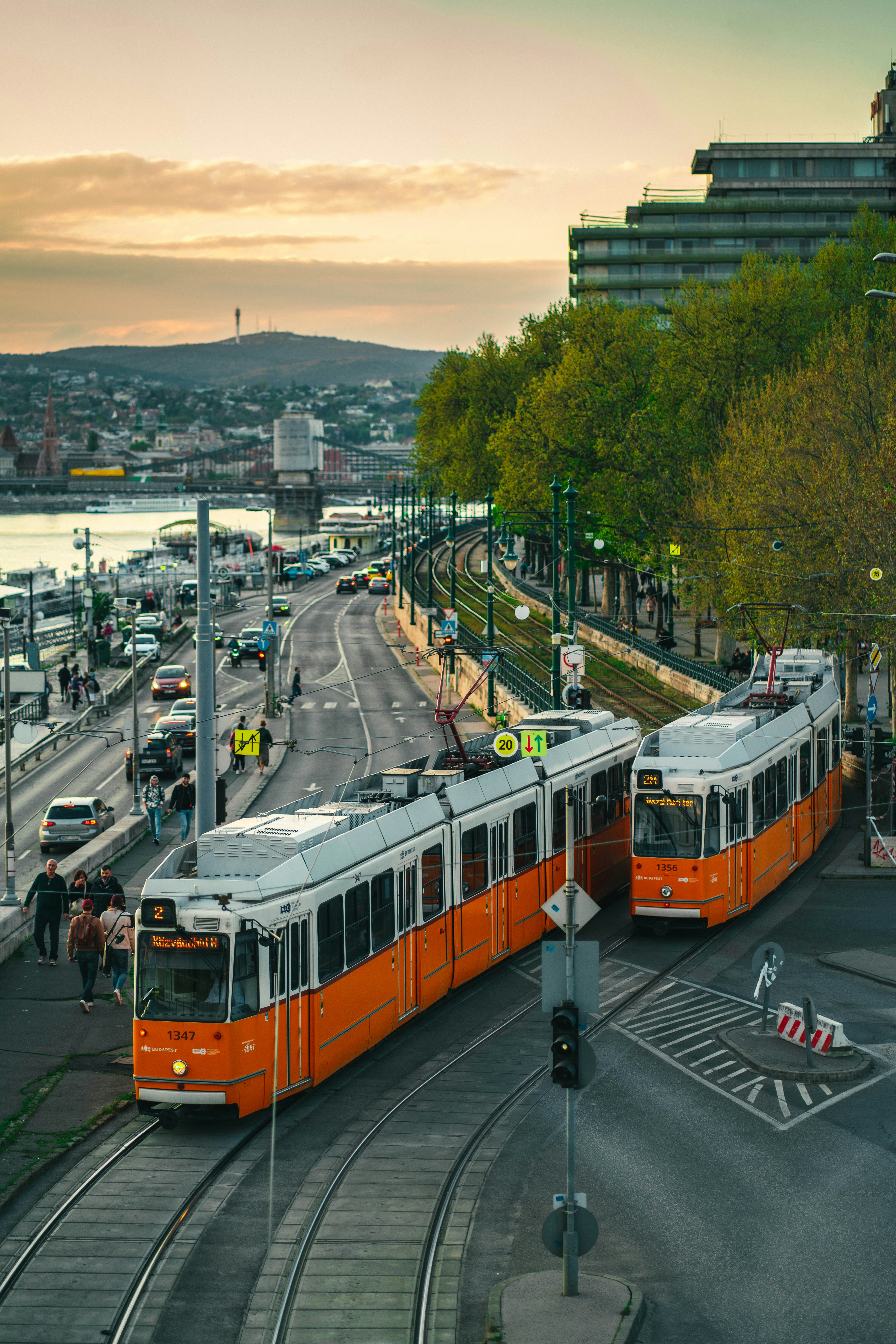 Twin Orange Trams Parade Along a Riverside Street at Dusk