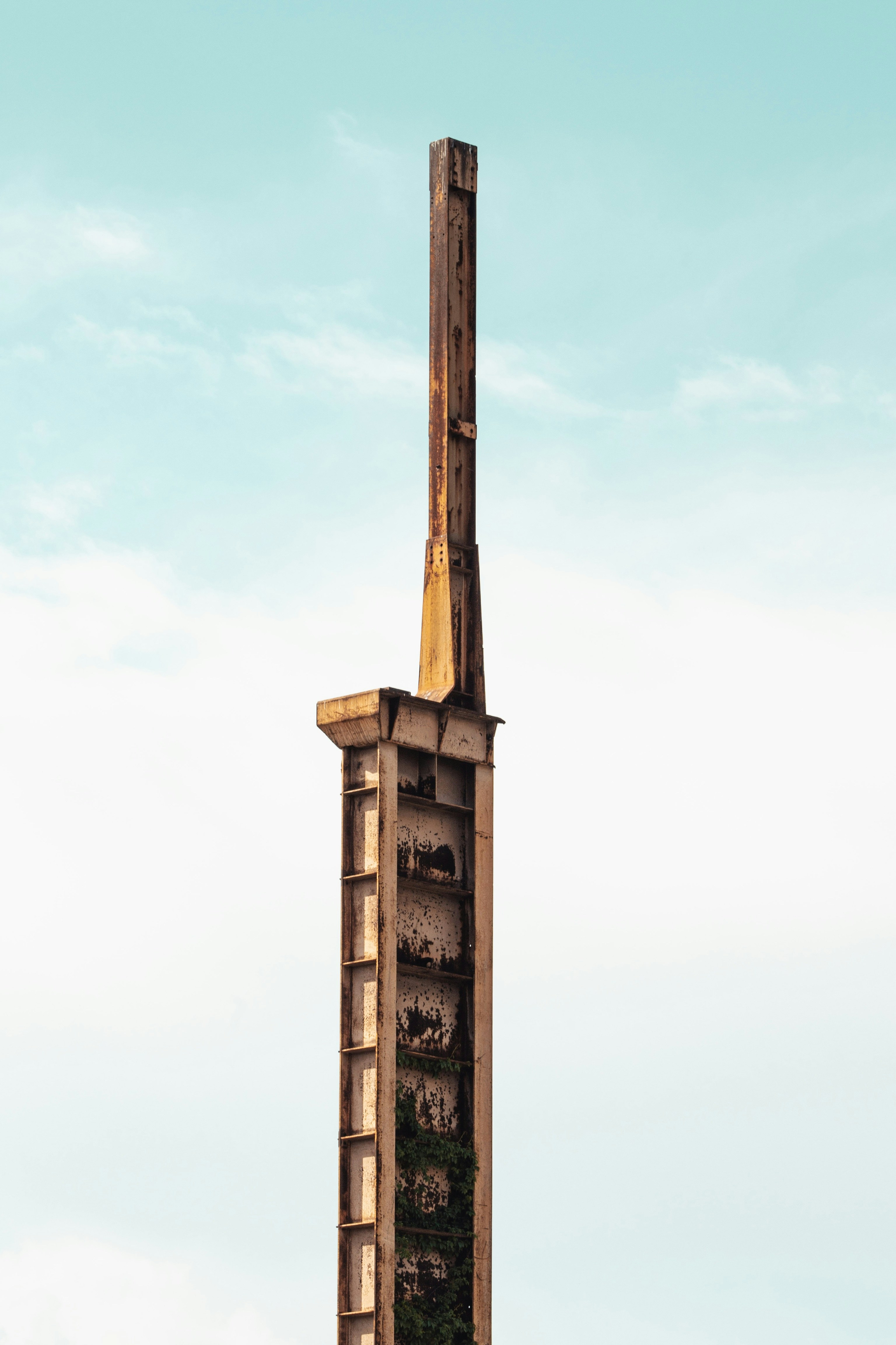 An aged, vertical concrete structure with patches of greenery against a clear blue sky, illustrating nature's reclamation of man-made forms.