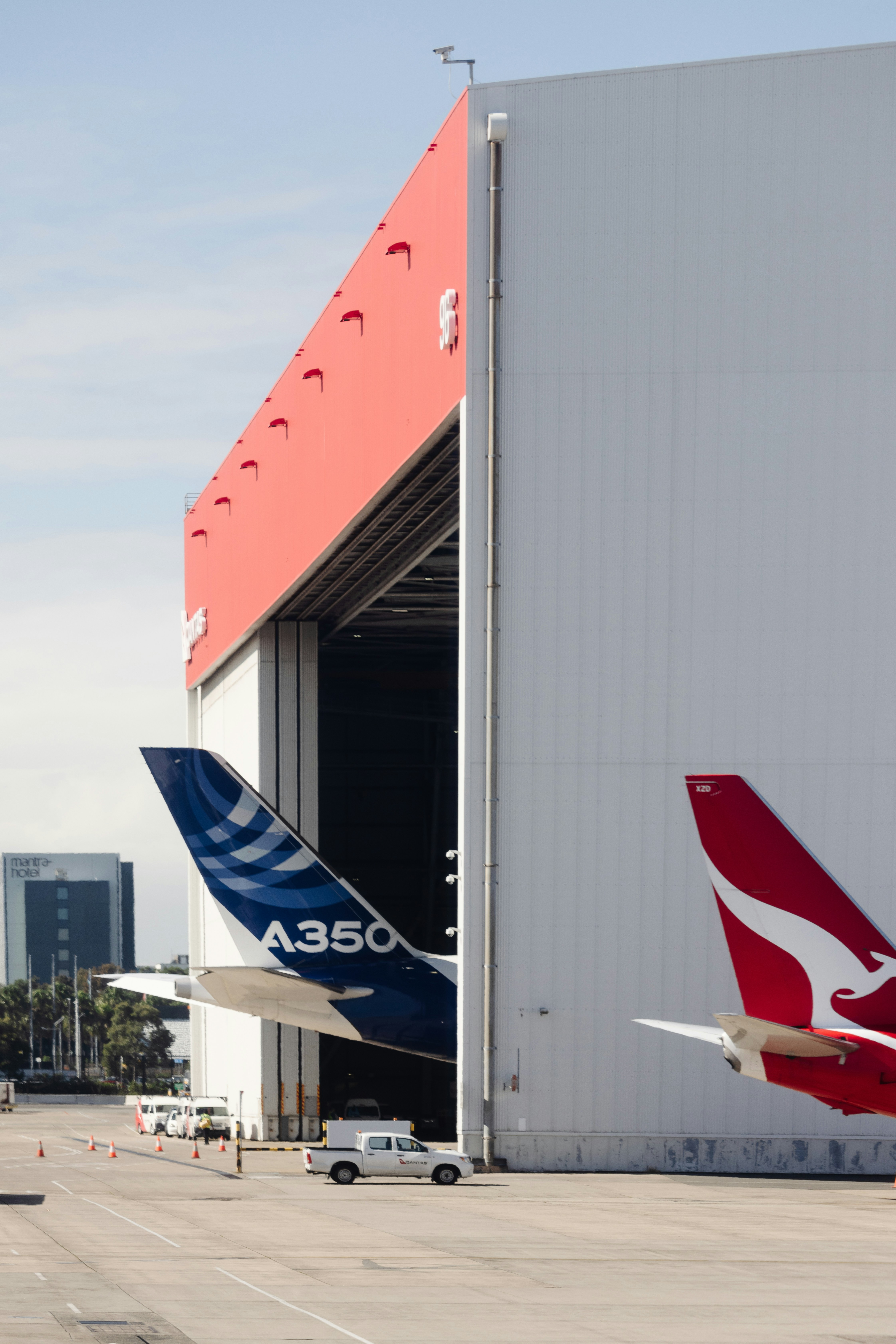 The tails of an A350 and a Qantas aircraft peek out from a hangar, showcasing their distinctive designs against a modern backdrop.