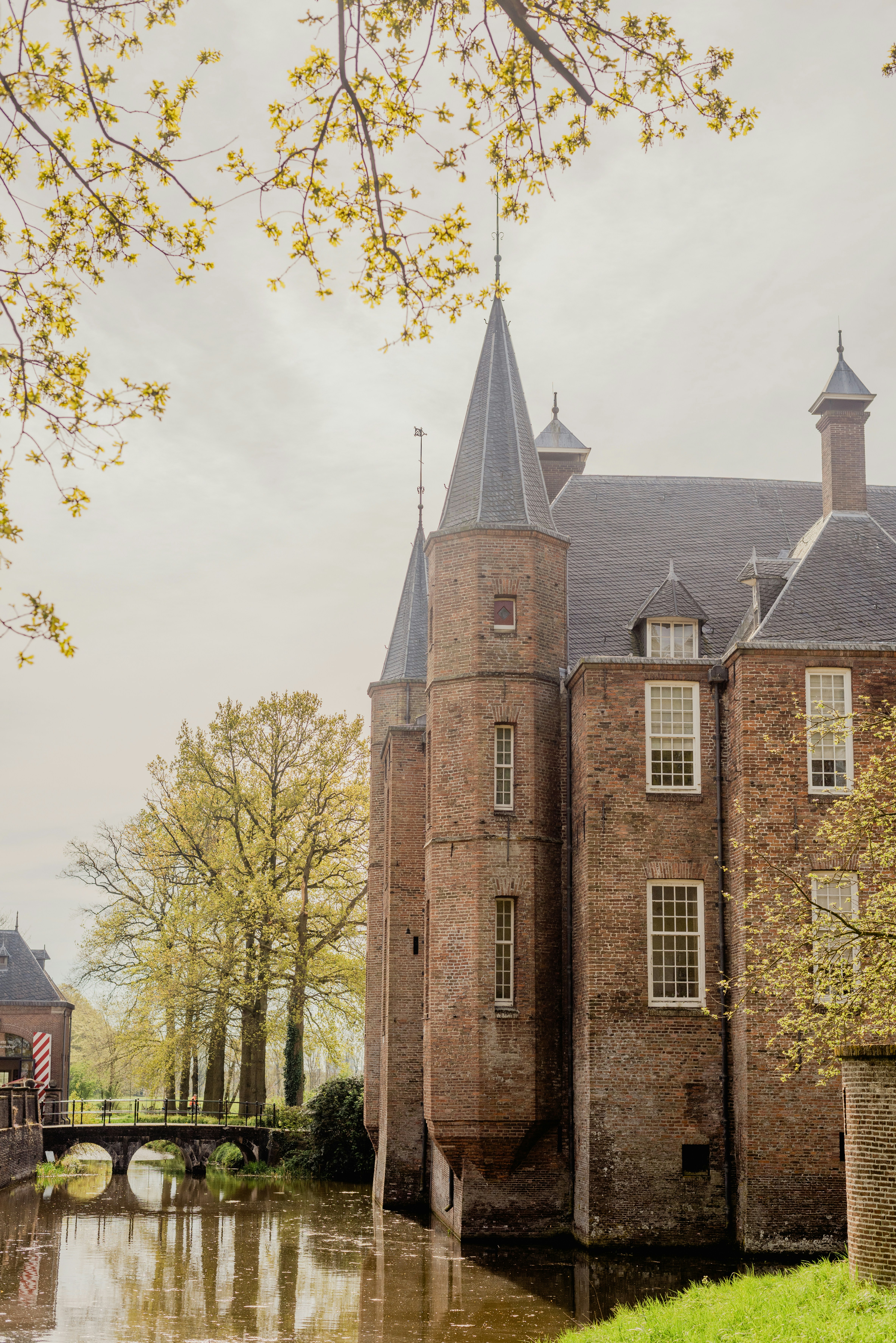 A medieval castle stands resilient by the tranquil waters, framed by lush greenery and soft spring light.