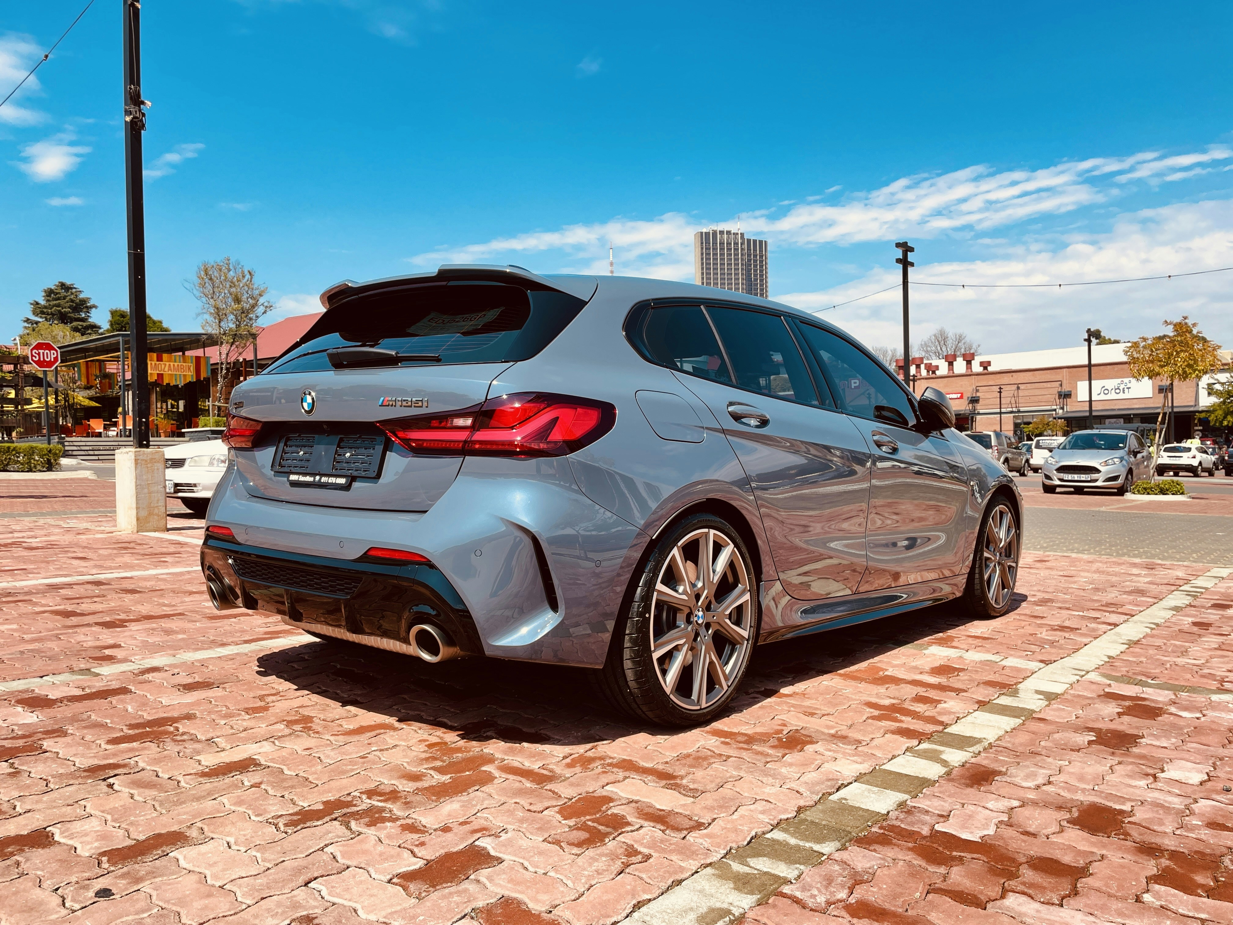 Chrome Blue Hatchback Anchors a Brick-Paved Mall Parking Lot under a Clear Sky