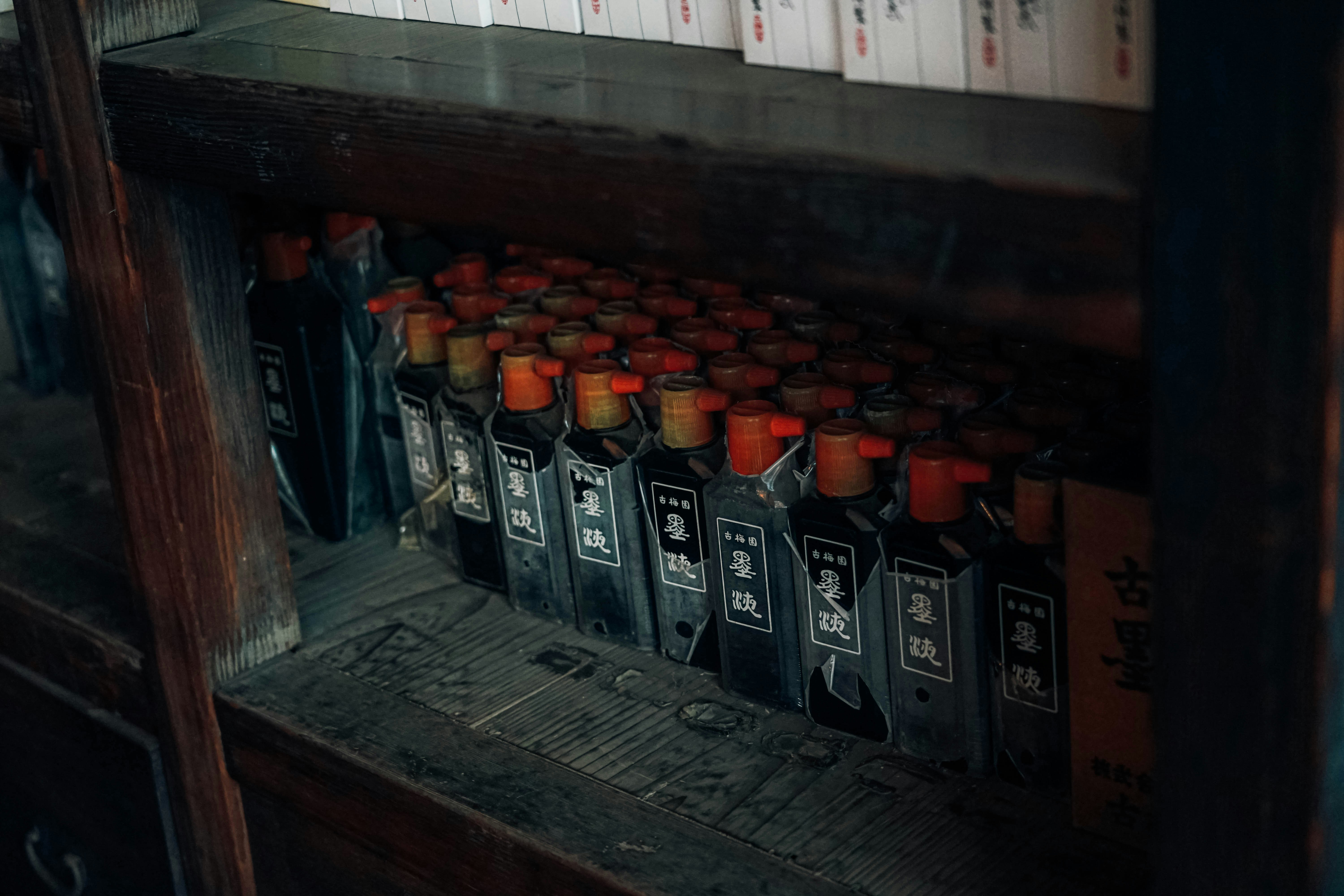 Red-Capped Bottles on a Weathered Wooden Shelf: A Quiet Still-Life in Shadow