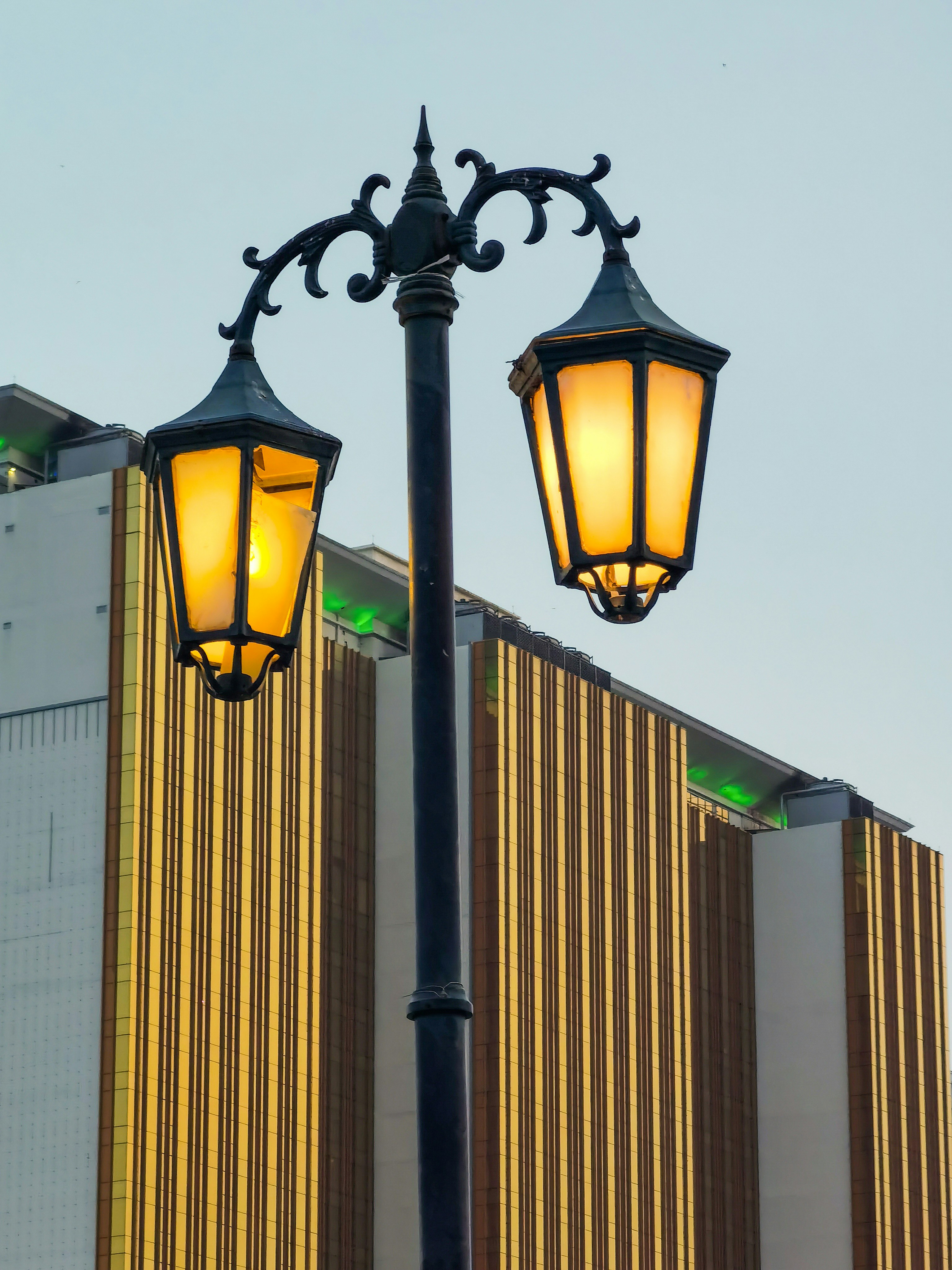 Vintage street lamps glow warmly against a modern architectural backdrop, highlighting the contrast between old and new.