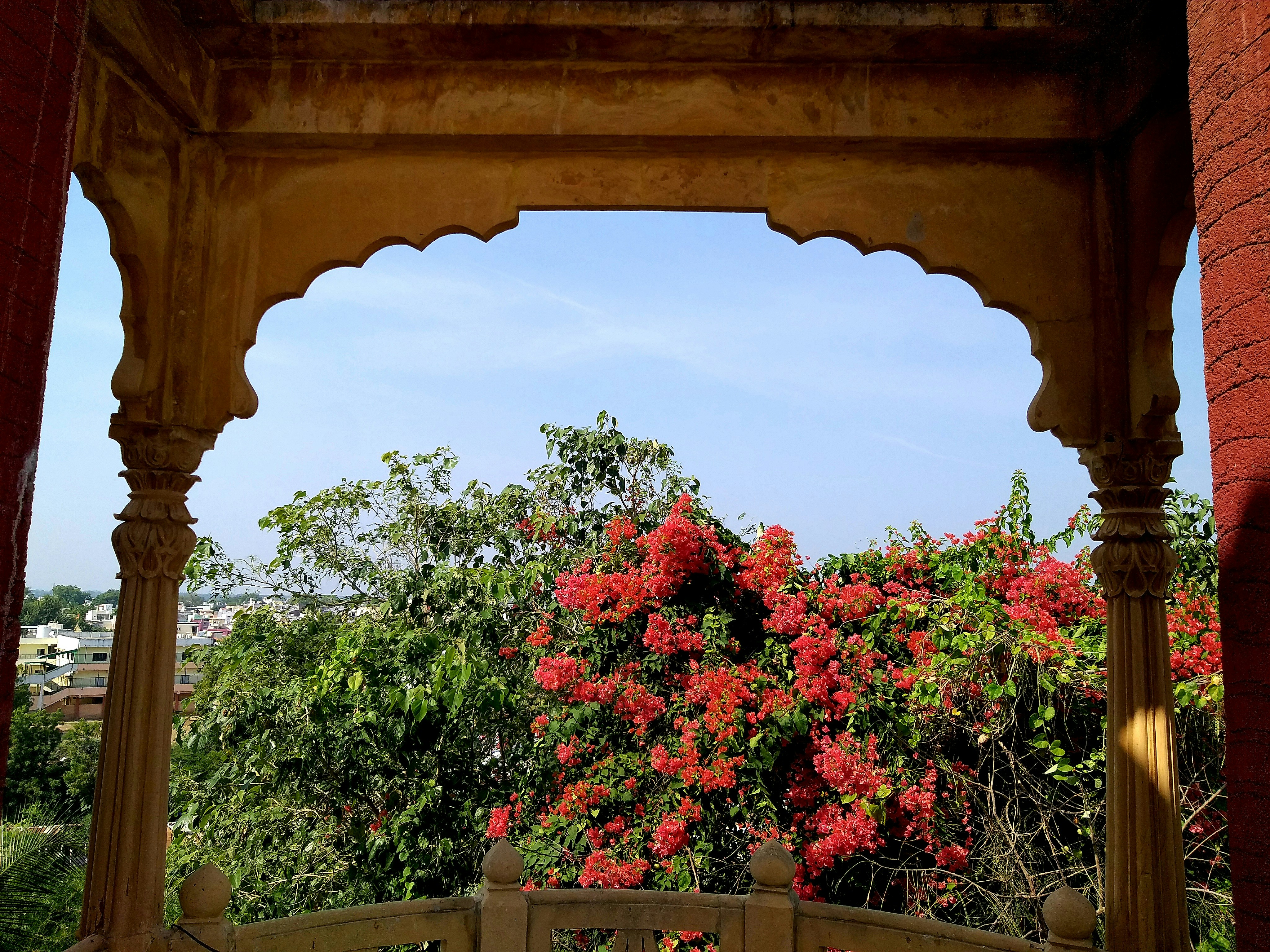 Intricate architectural archway framing vibrant bougainvillea blooms against a clear blue sky.