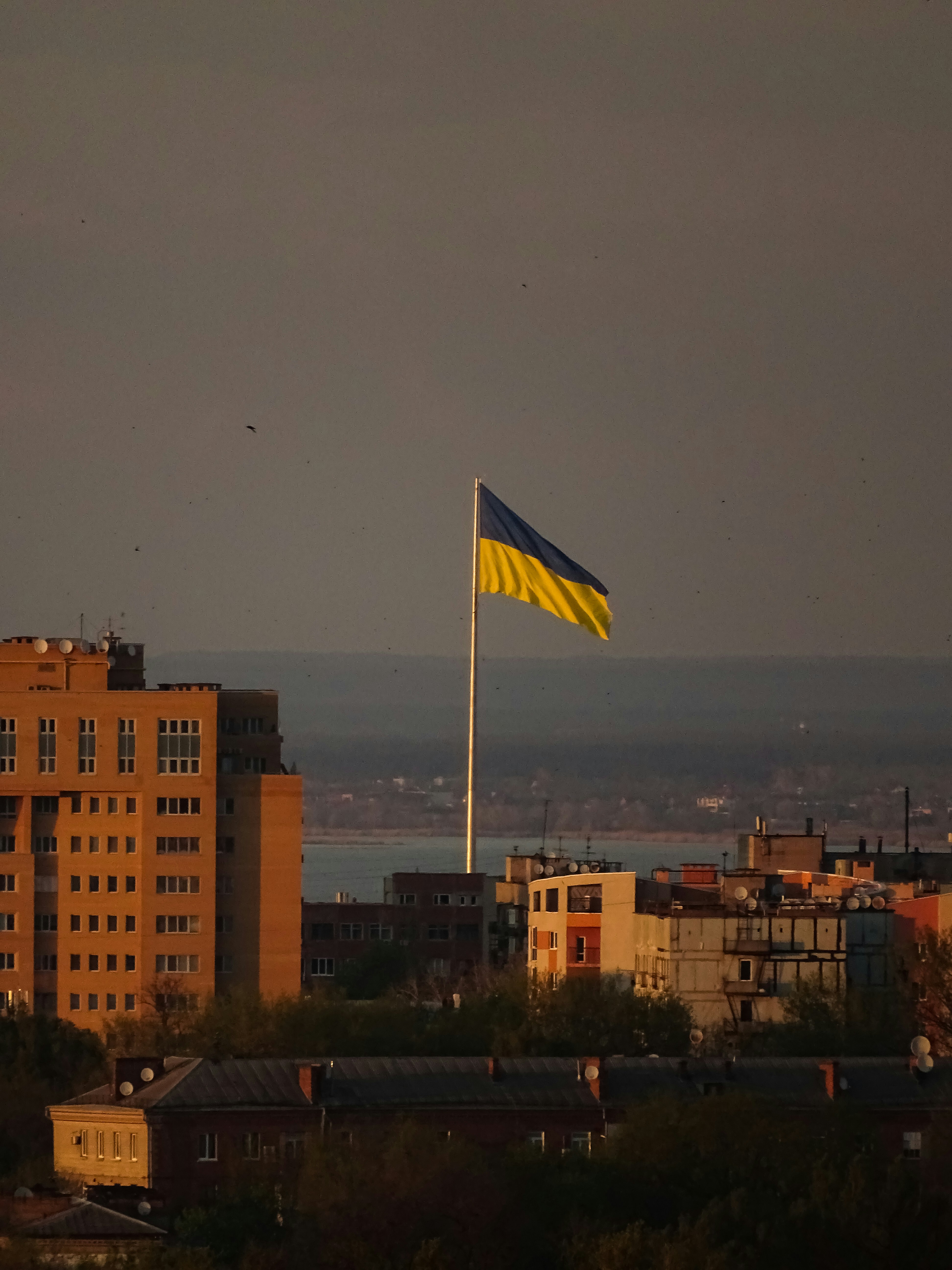 Flag over the city: Ukrainian tricolor fluttering above a quiet urban horizon