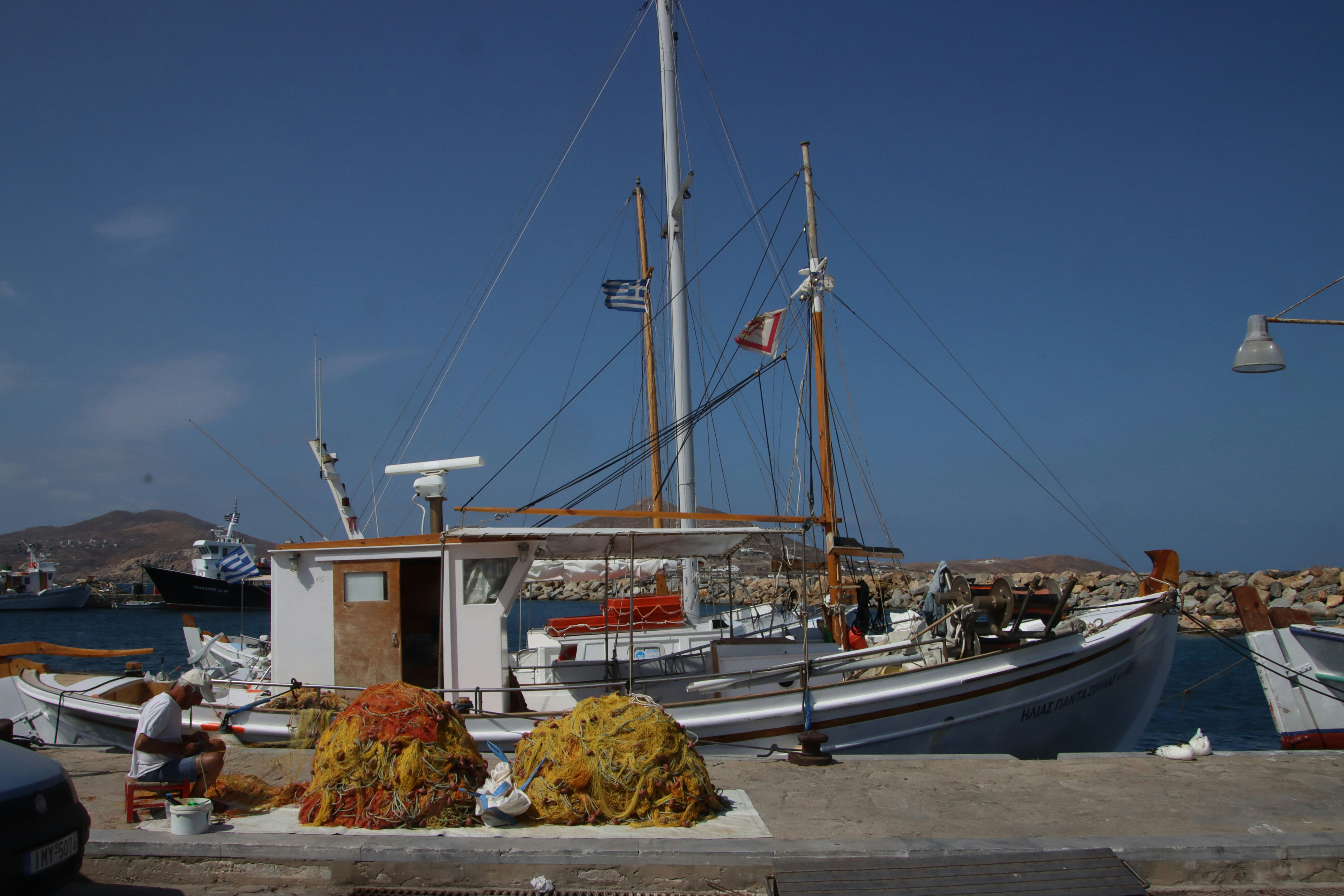 Traditional fishing boat docked in a lively harbor, surrounded by colorful nets and distant vessels. The scene reflects the essence of coastal living.