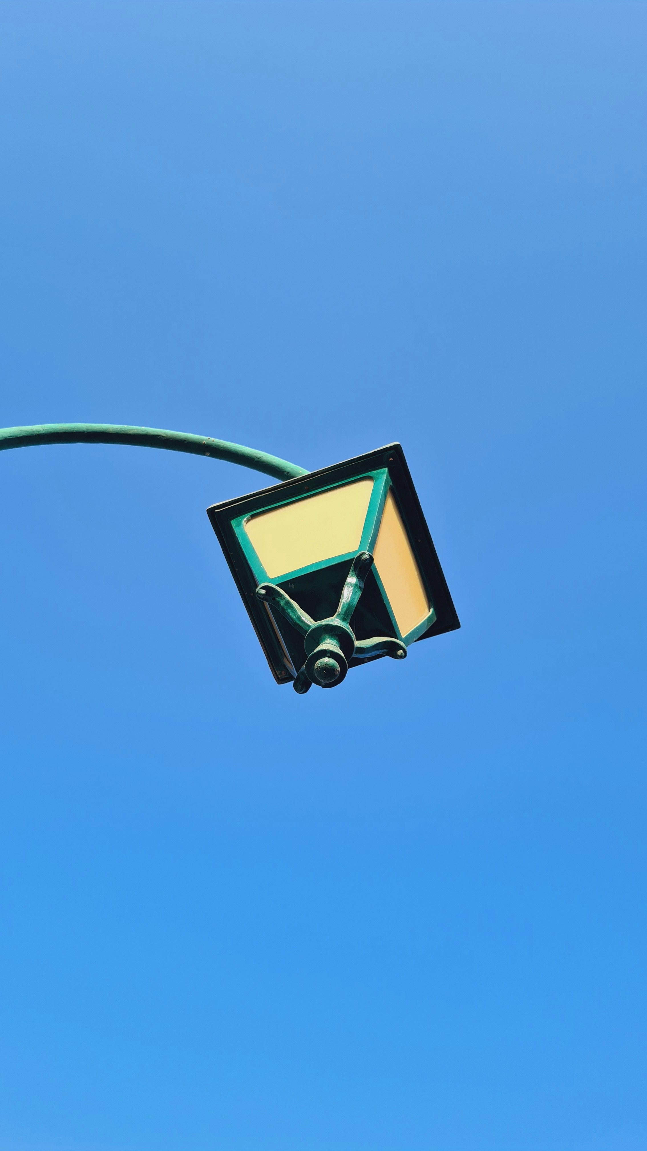 A vintage-style street lamp suspended against a clear blue sky, showcasing its unique design and functionality.