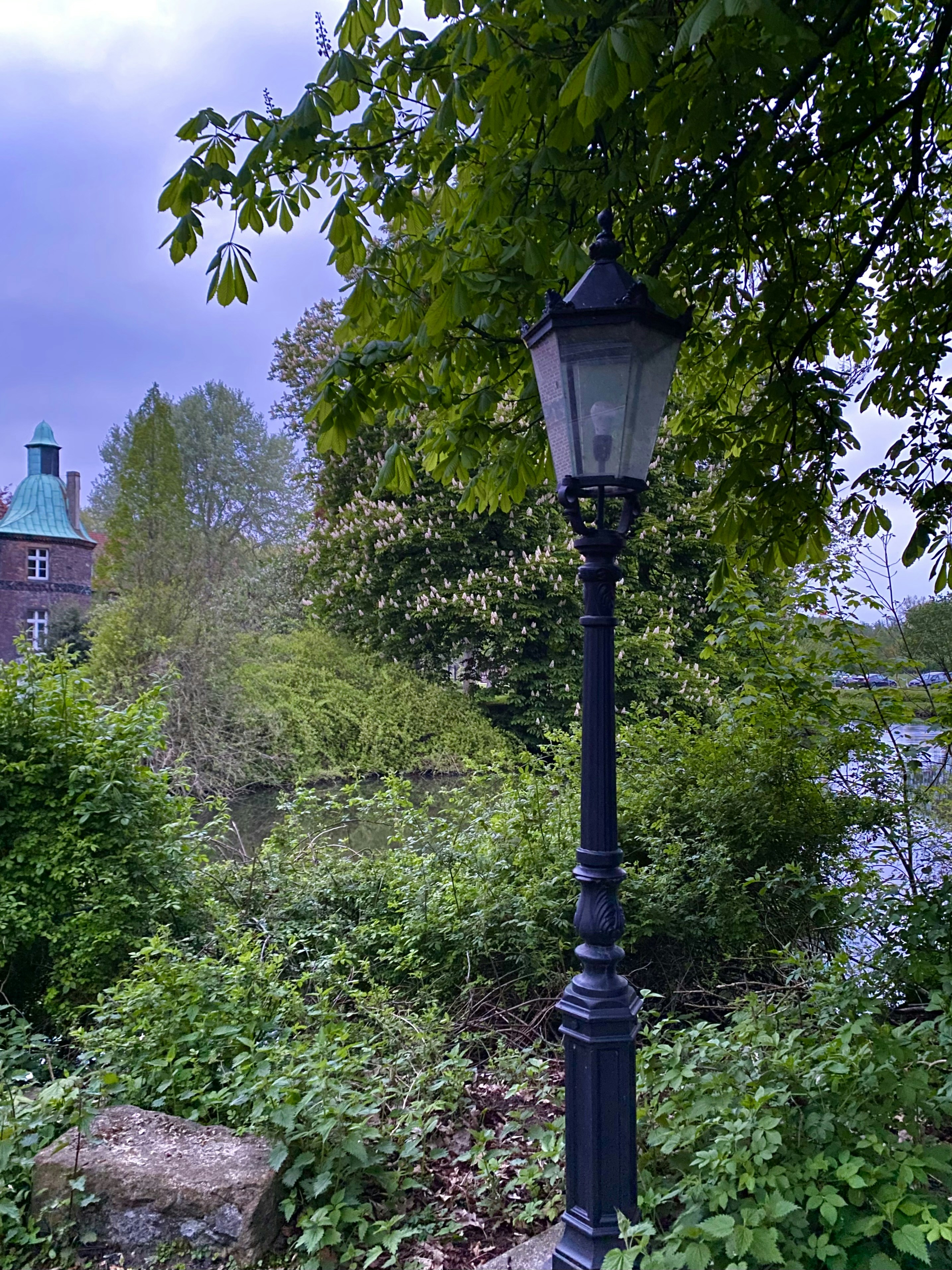 Vintage lamppost surrounded by lush greenery near a tranquil waterway, evoking a peaceful ambiance.
