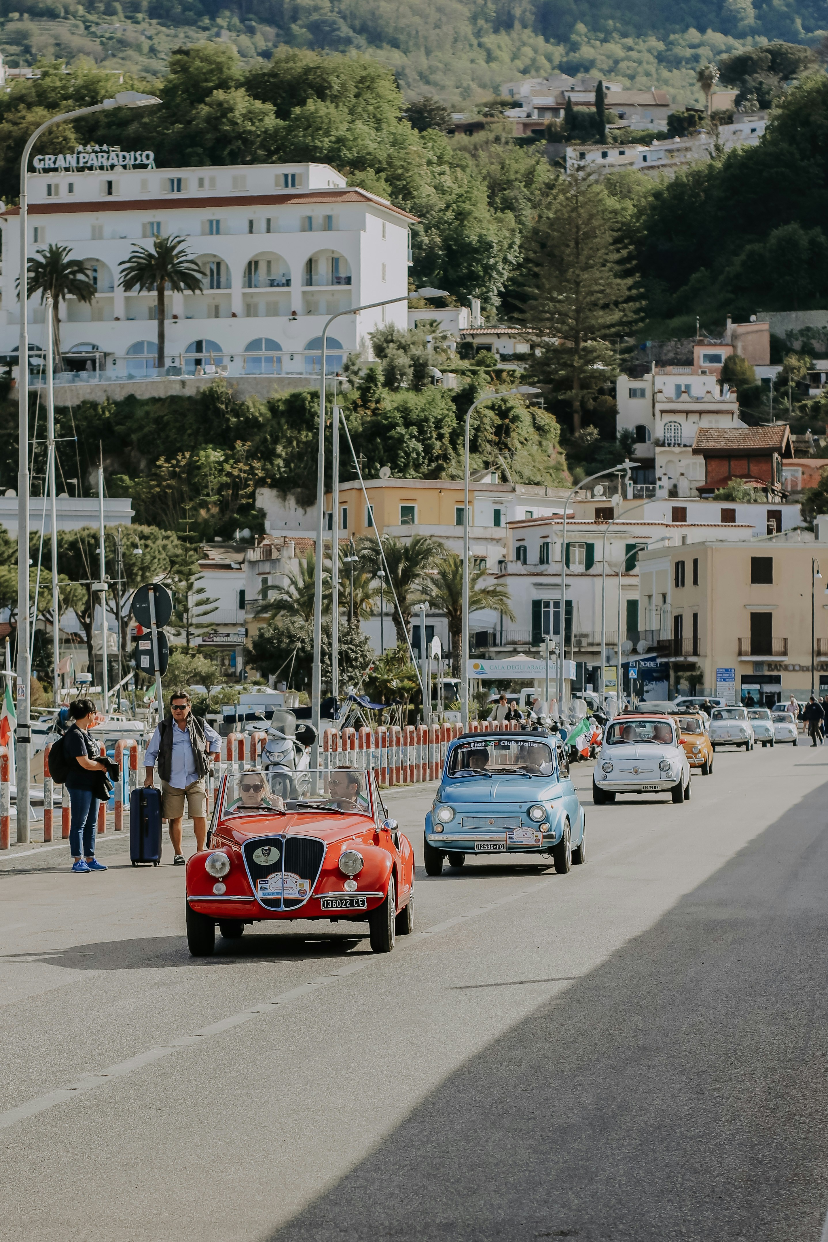 Sunlit Coast Car Parade: A Red Classic Leads the Street
