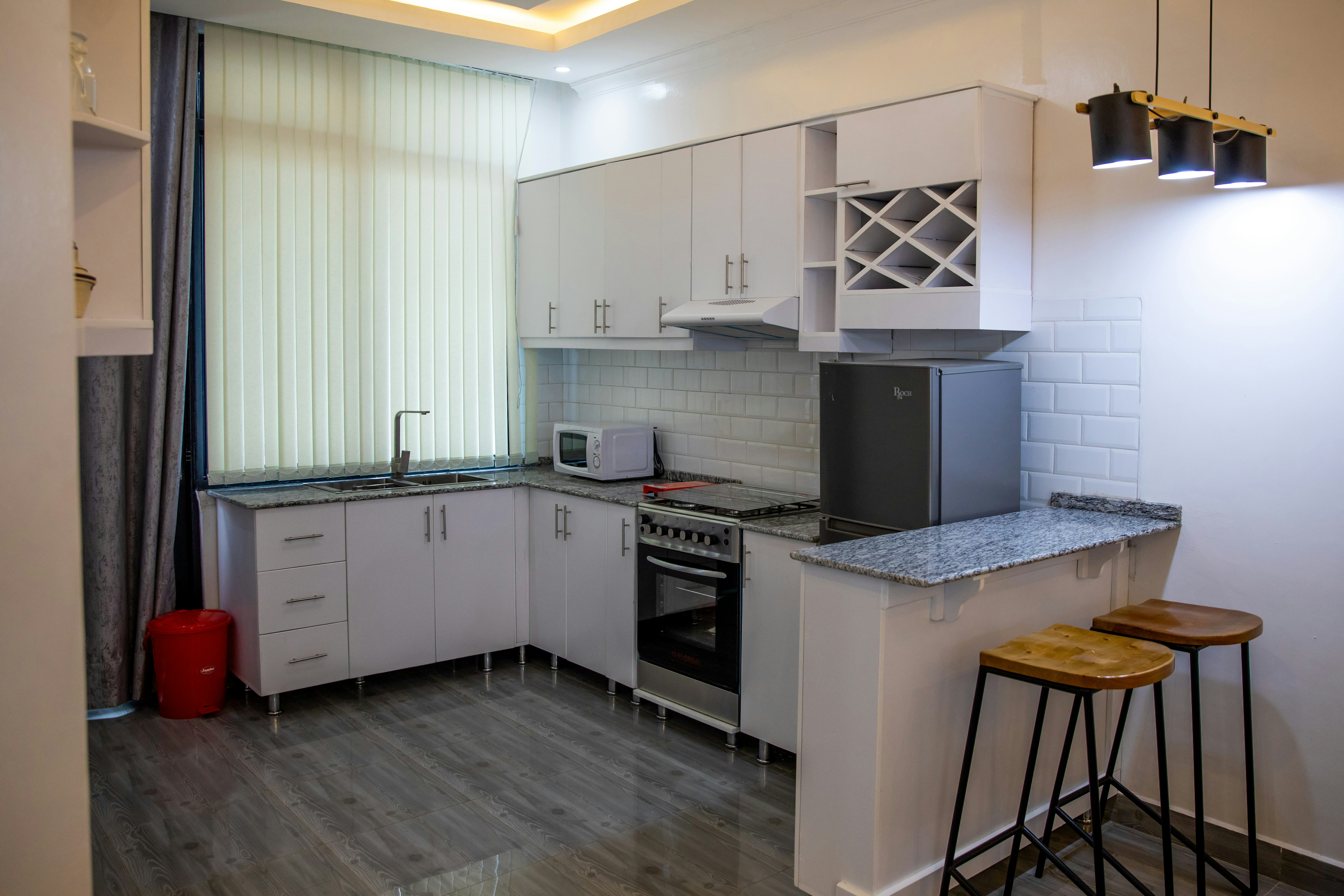 Contemporary kitchen featuring sleek white cabinets, a stainless steel refrigerator, and wooden stools under pendant lighting.