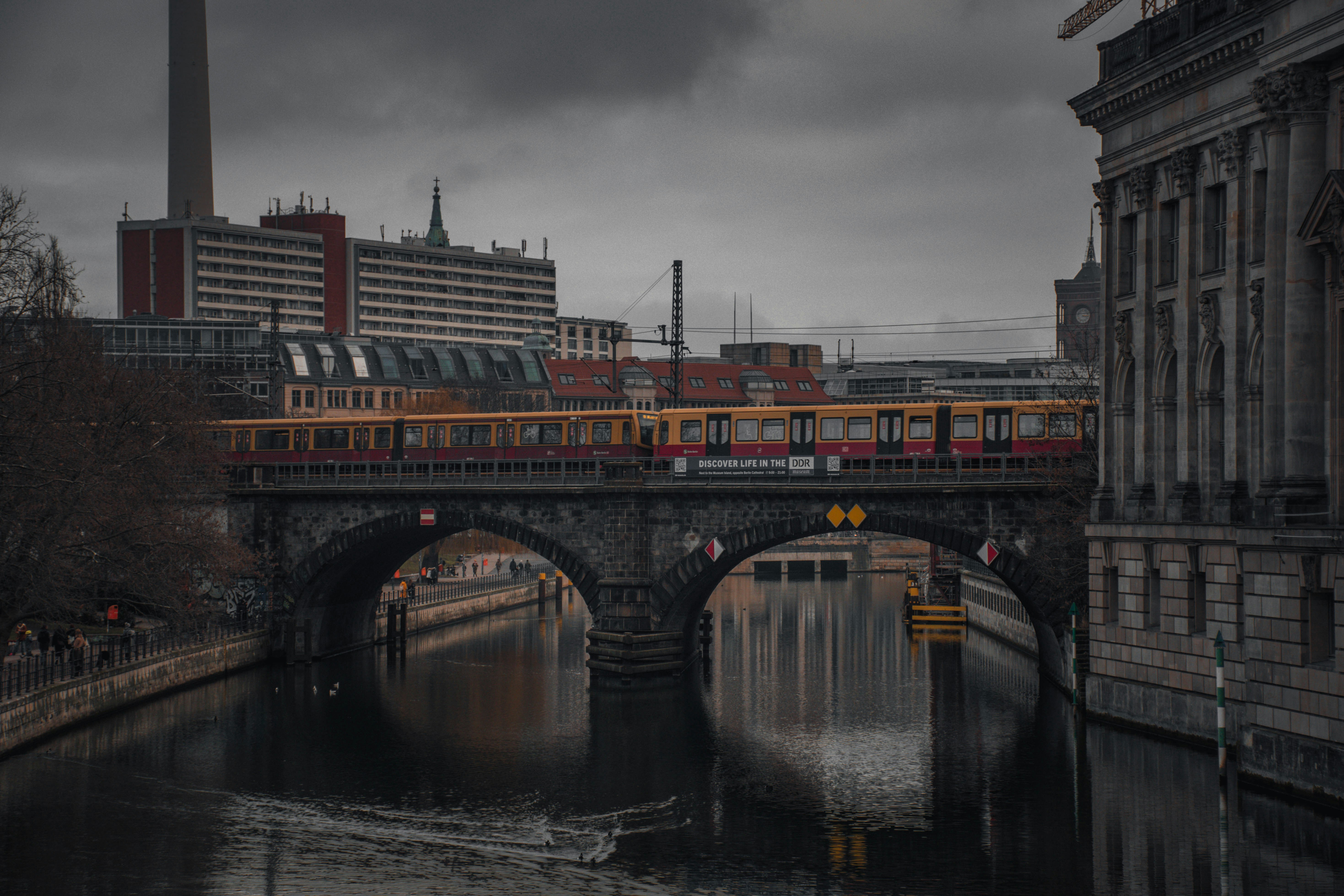 Urban Rail at the Arched Bridge: Train Crossing a Cloudy Canal