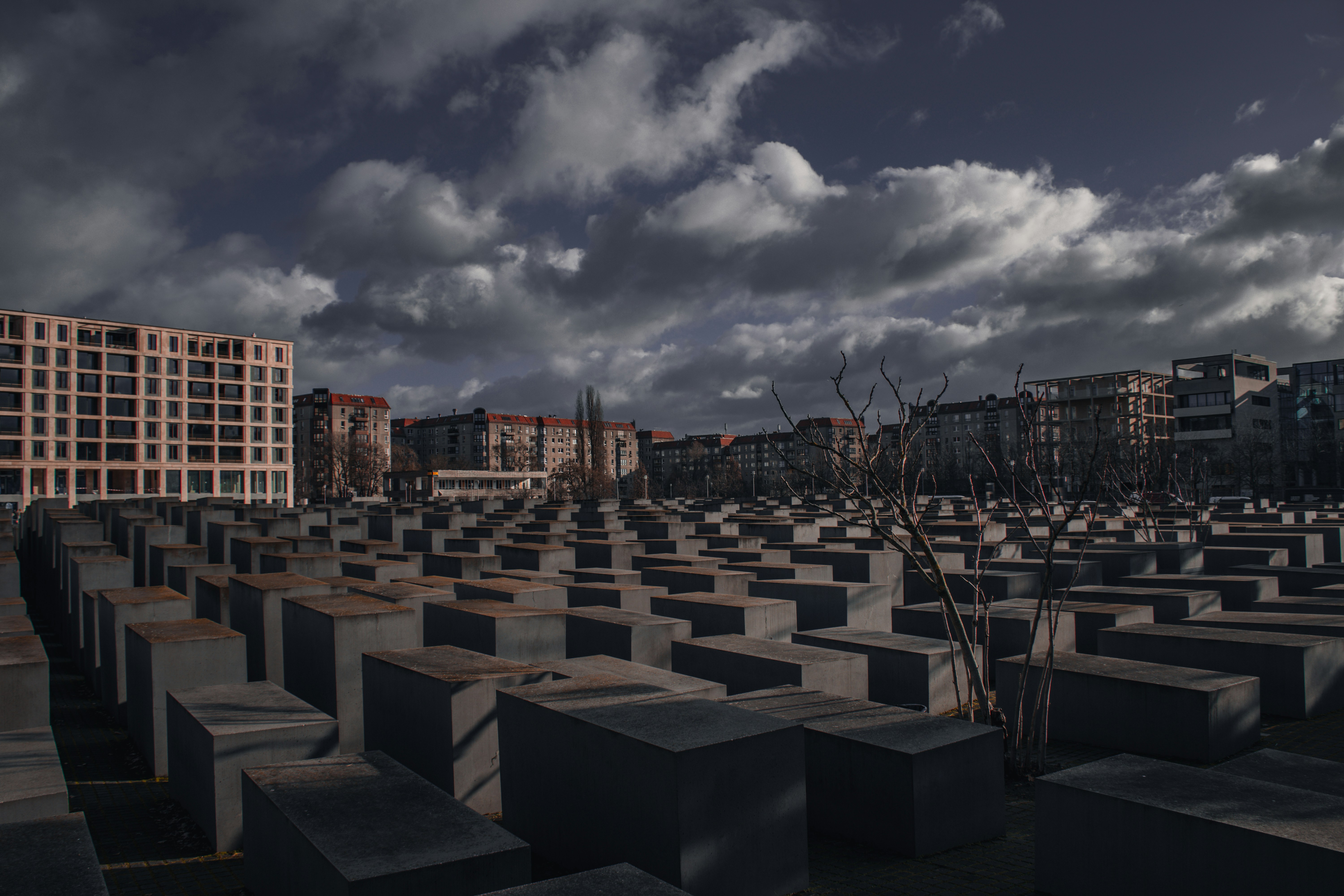 Grid of Memory: Concrete Cubes Beneath a Cloud-Charged Skyline