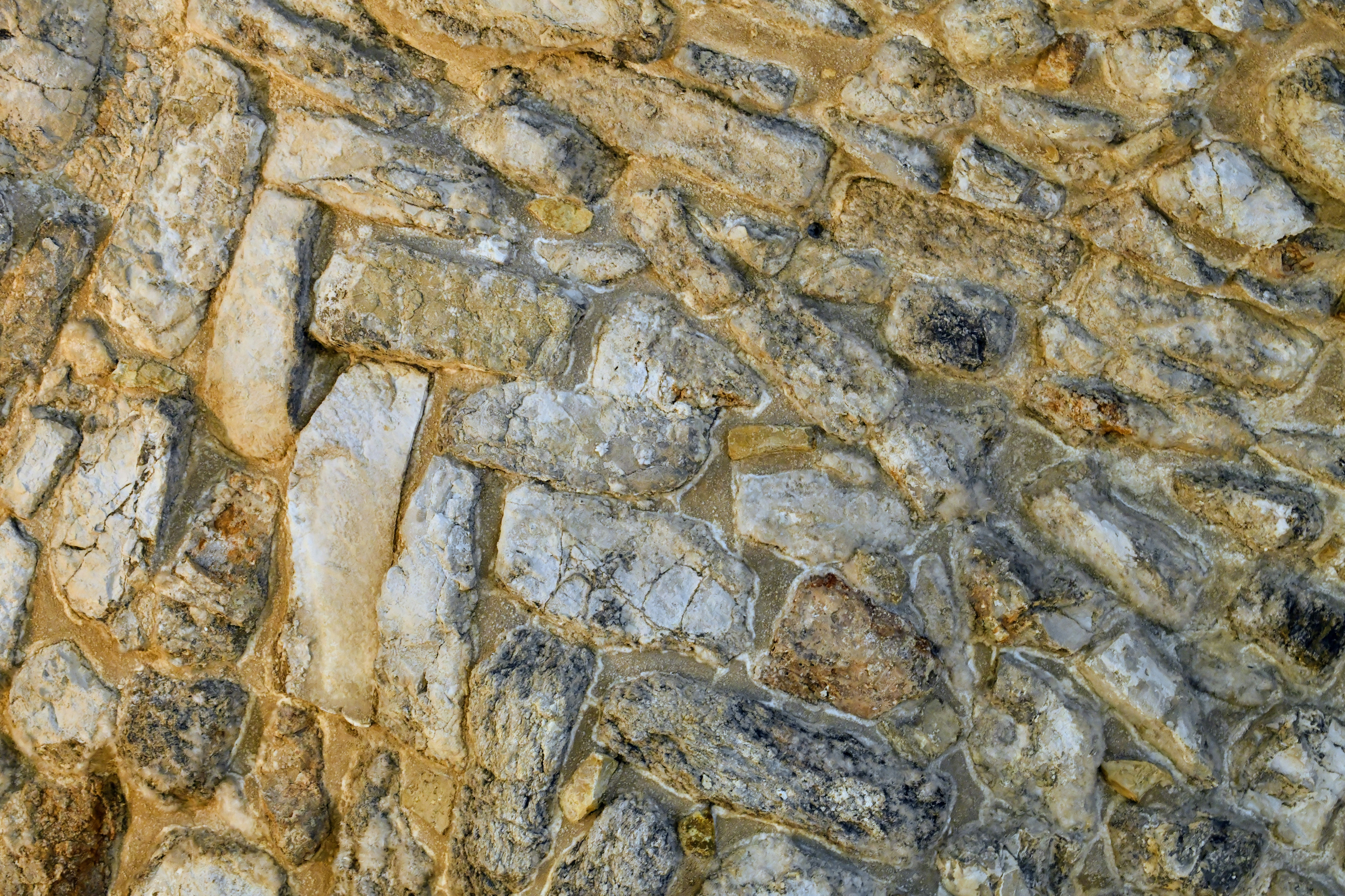 Close-up view of an intricately arranged stone wall, showcasing various textures and colors of the stones. The composition highlights the natural beauty and craftsmanship of the stonework.
