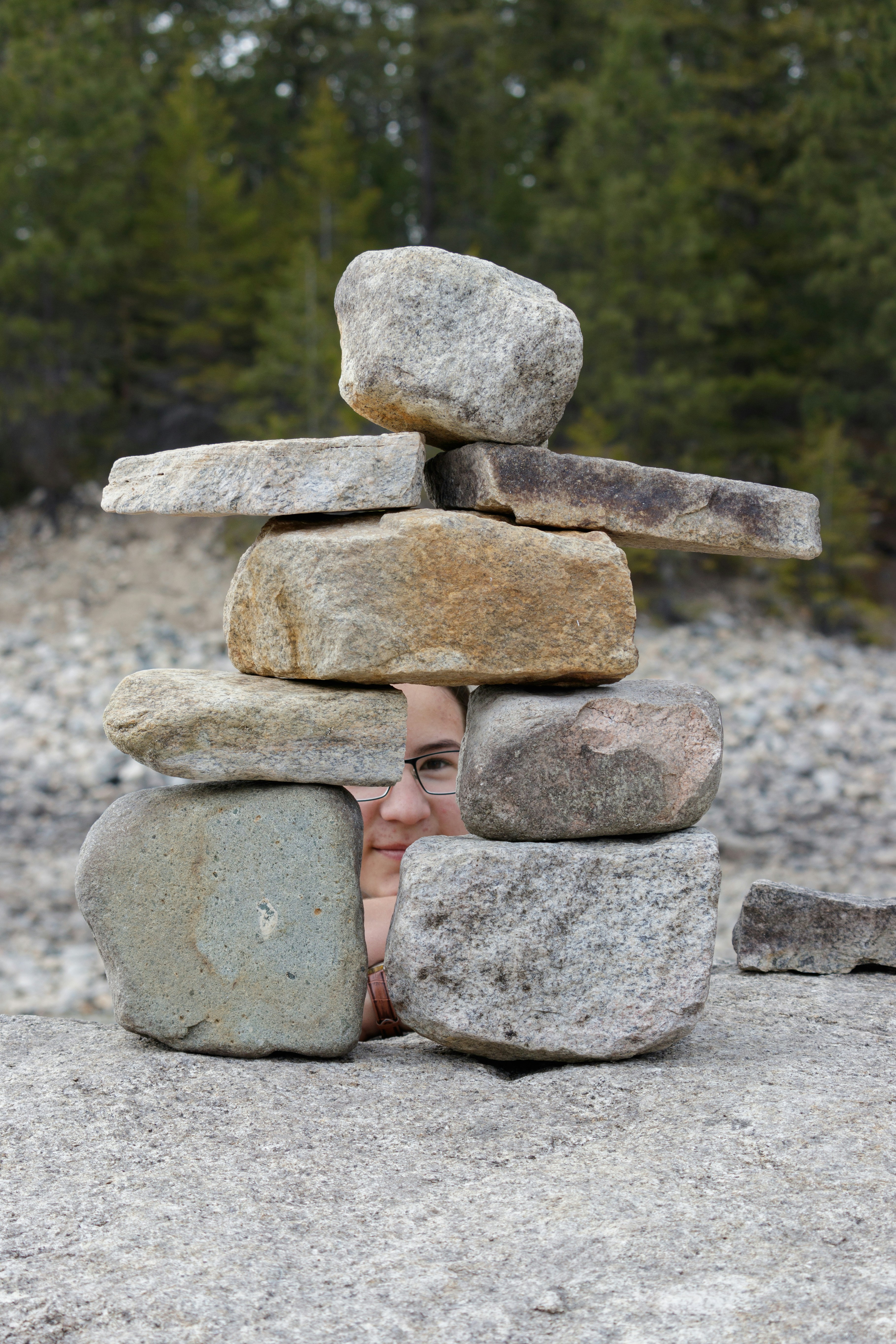 A stack of rocks forms a playful structure, partially concealing a person's face, blending human presence with natural elements.