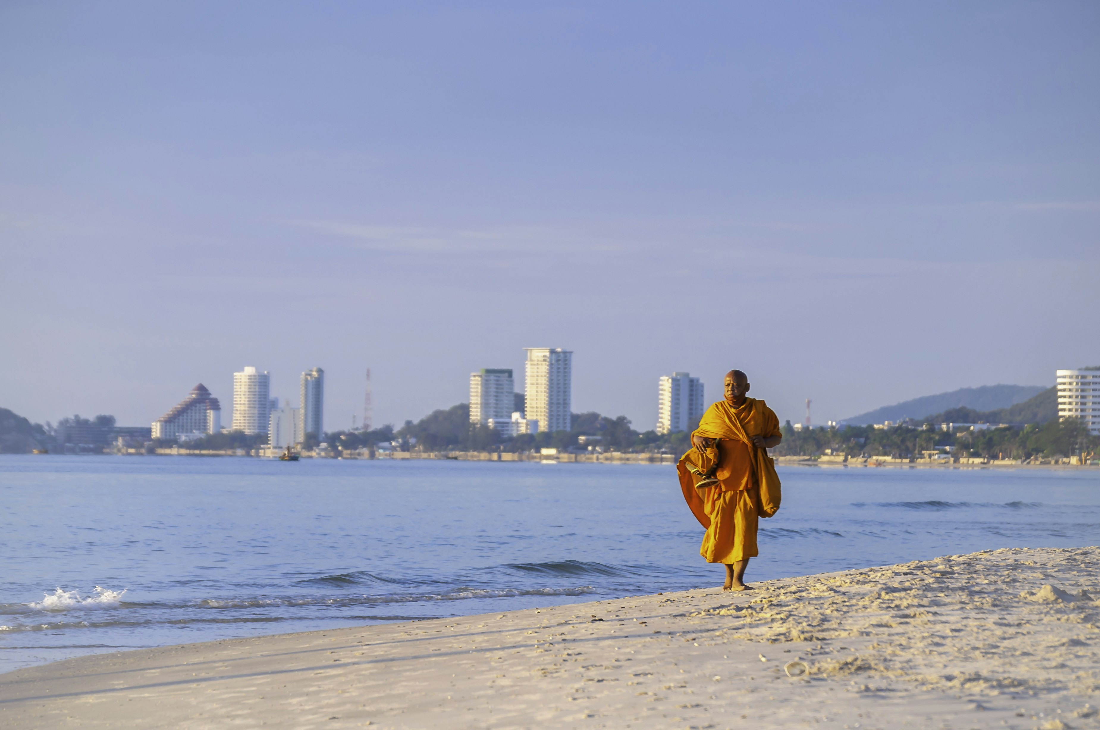 Orange-Robed Wanderer on a Quiet Beach Facing a Distant City Horizon
