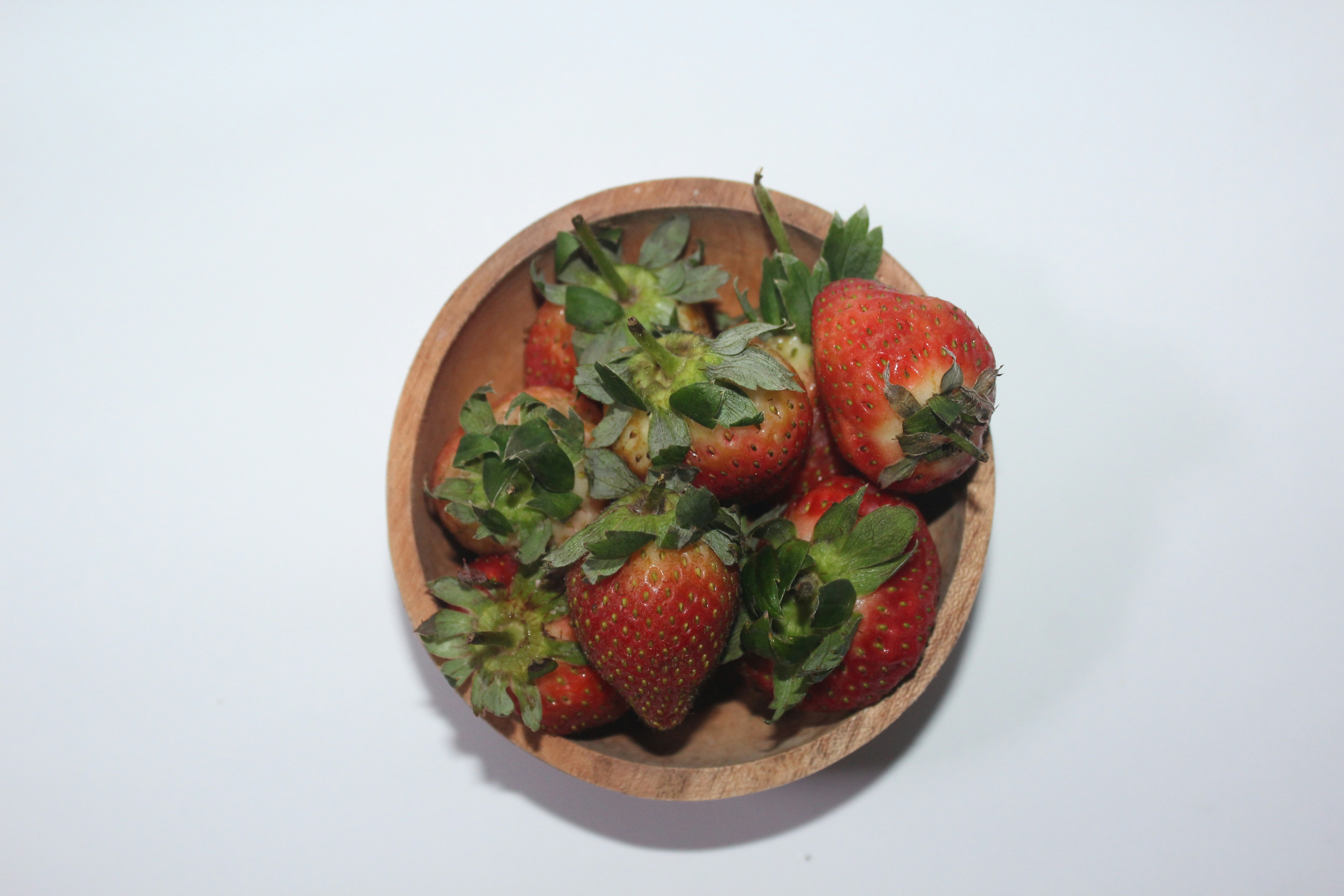 A wooden bowl filled with fresh strawberries, showcasing their vibrant red color and leafy green tops.