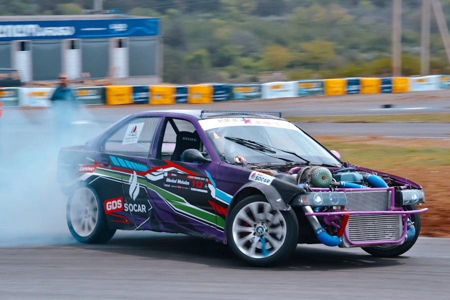 Purple drift car with exposed front intercooler and turbo piping sliding through blue tire smoke on a racetrack.