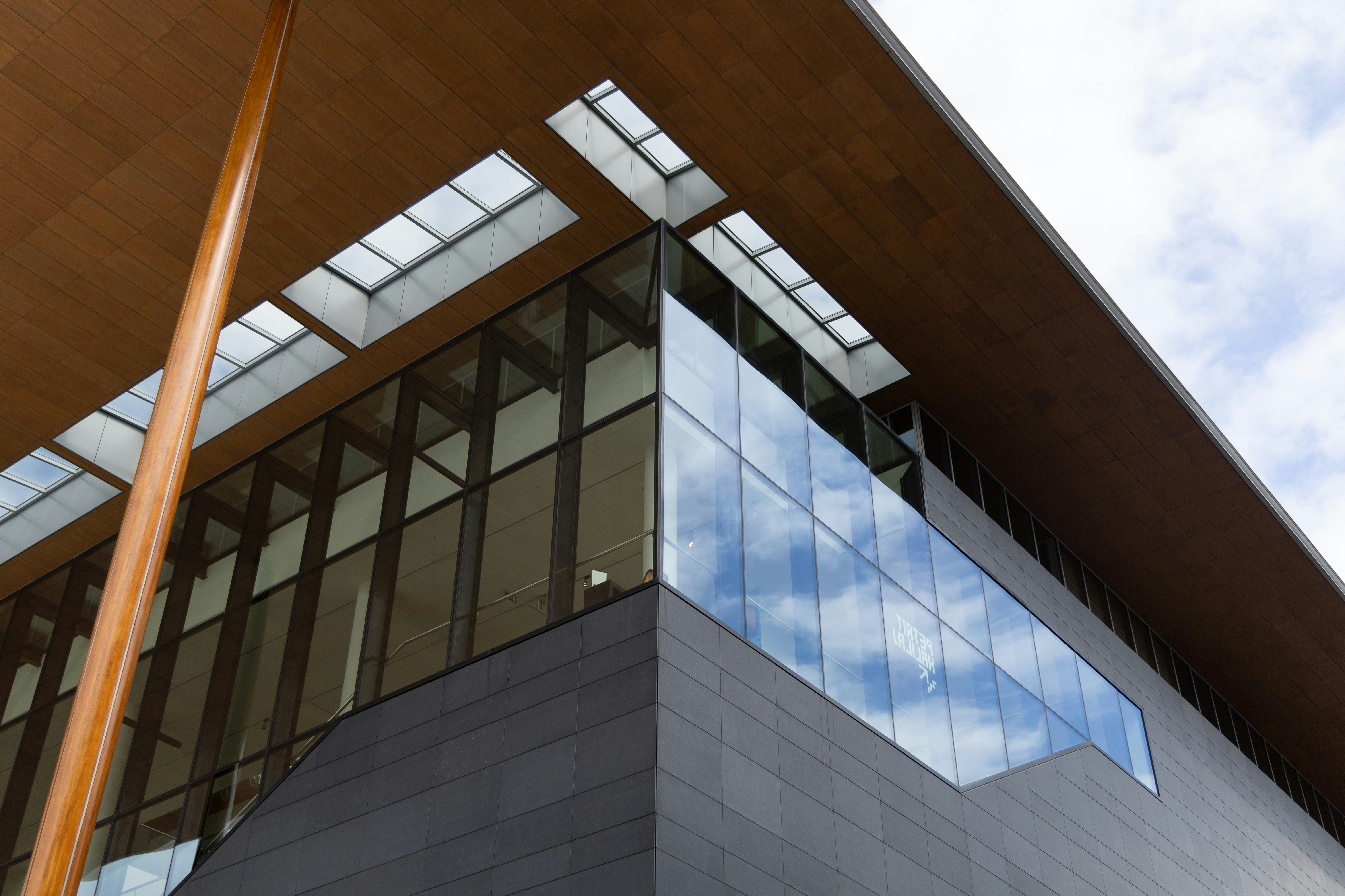 Contemporary building facade with reflective glass and angular lines against a partly cloudy sky.