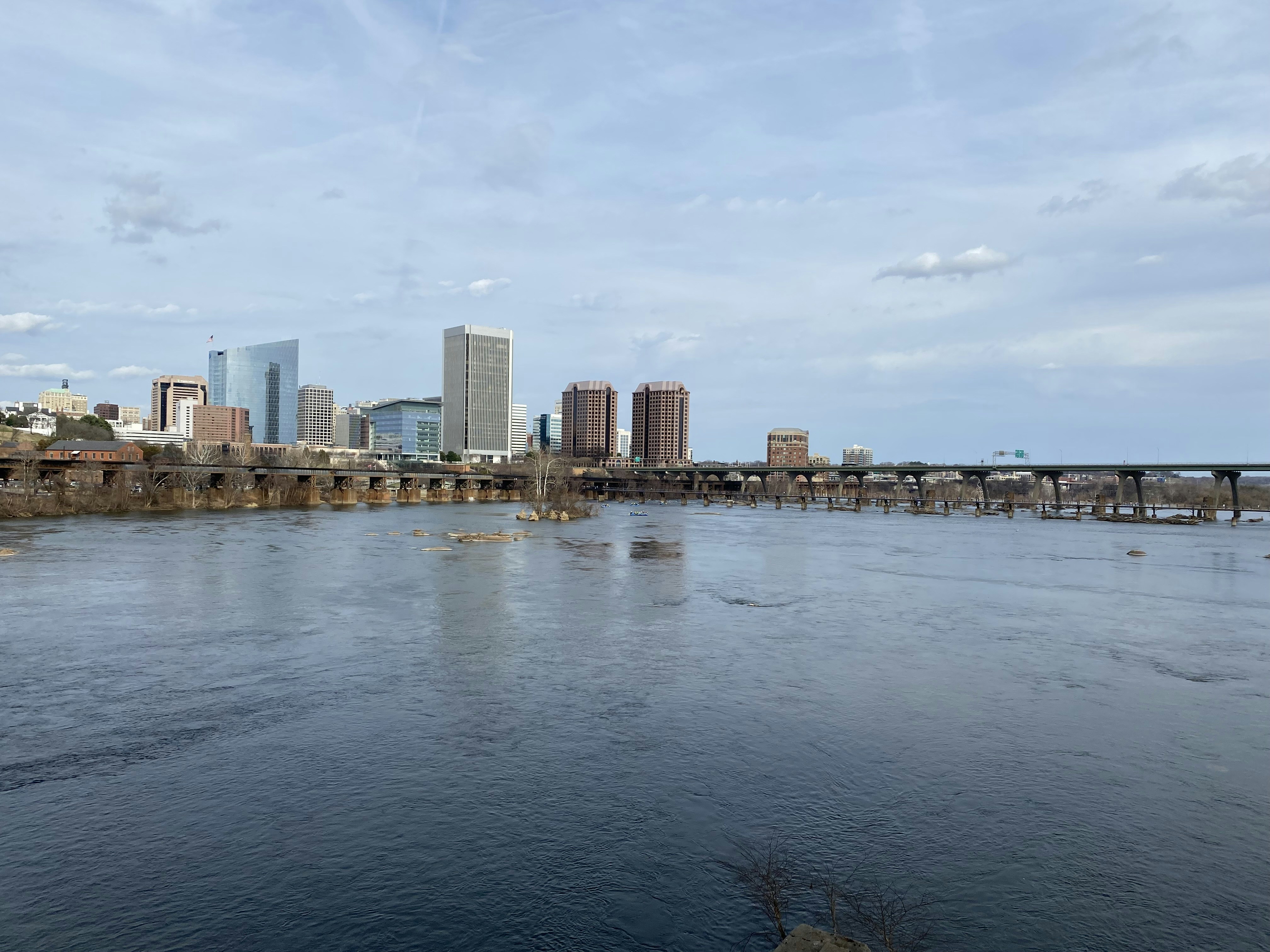 City skyline reflected in a calm river, showcasing modern architecture and bridges against a cloudy sky.