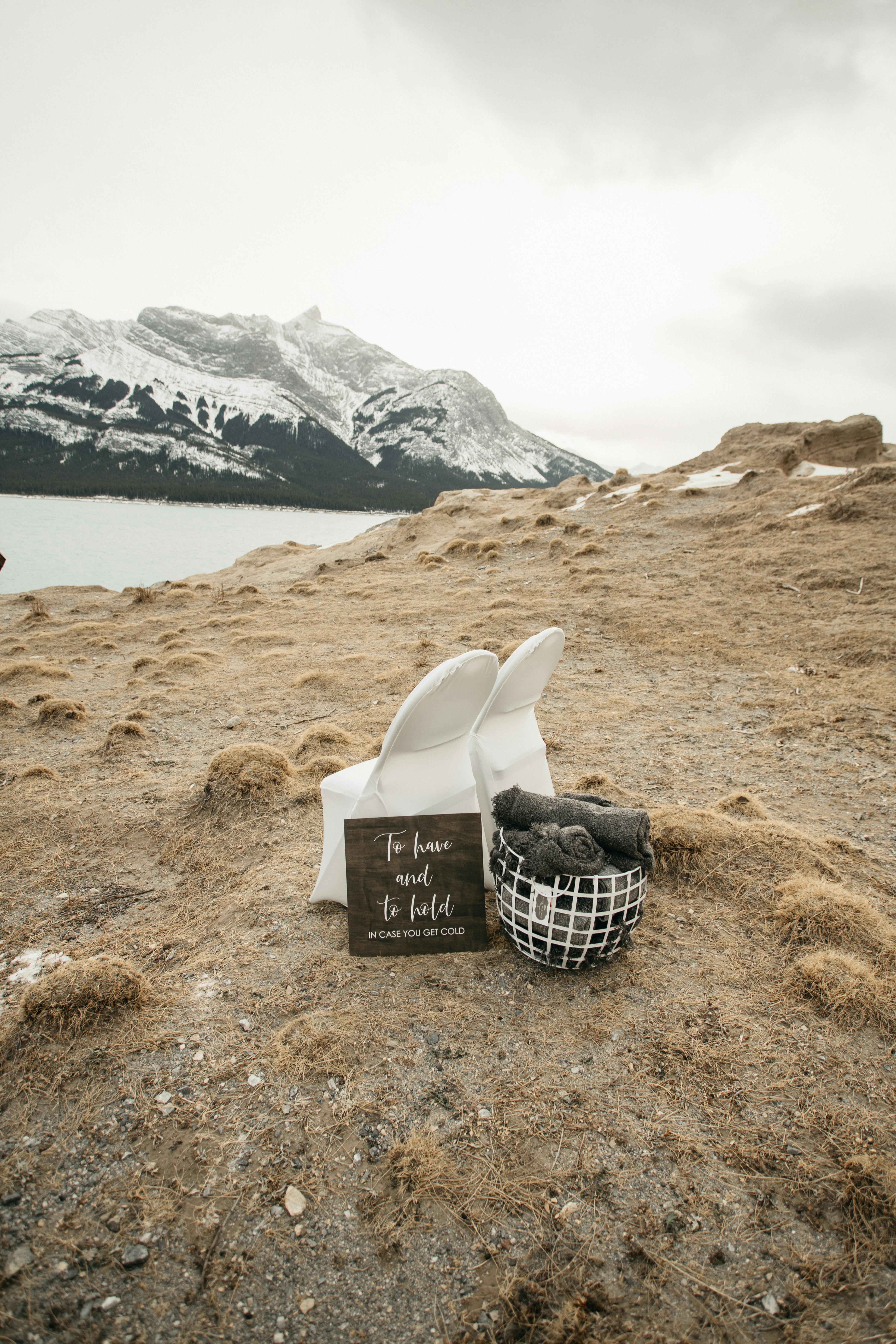 Deserted lakeside scene: white chairs and chalkboard sign by rugged shore