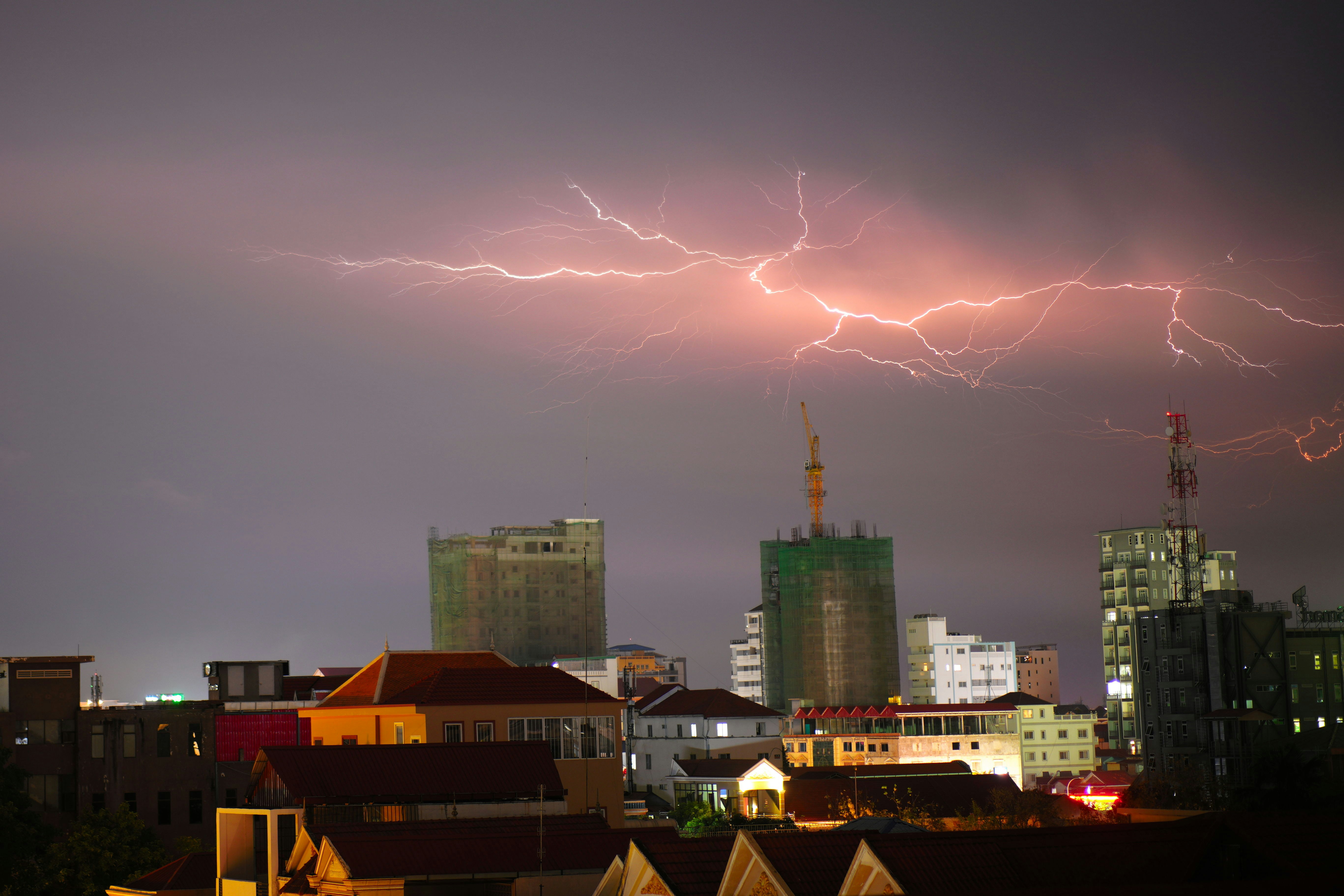 Lightning streaks across the night sky above illuminated city buildings.