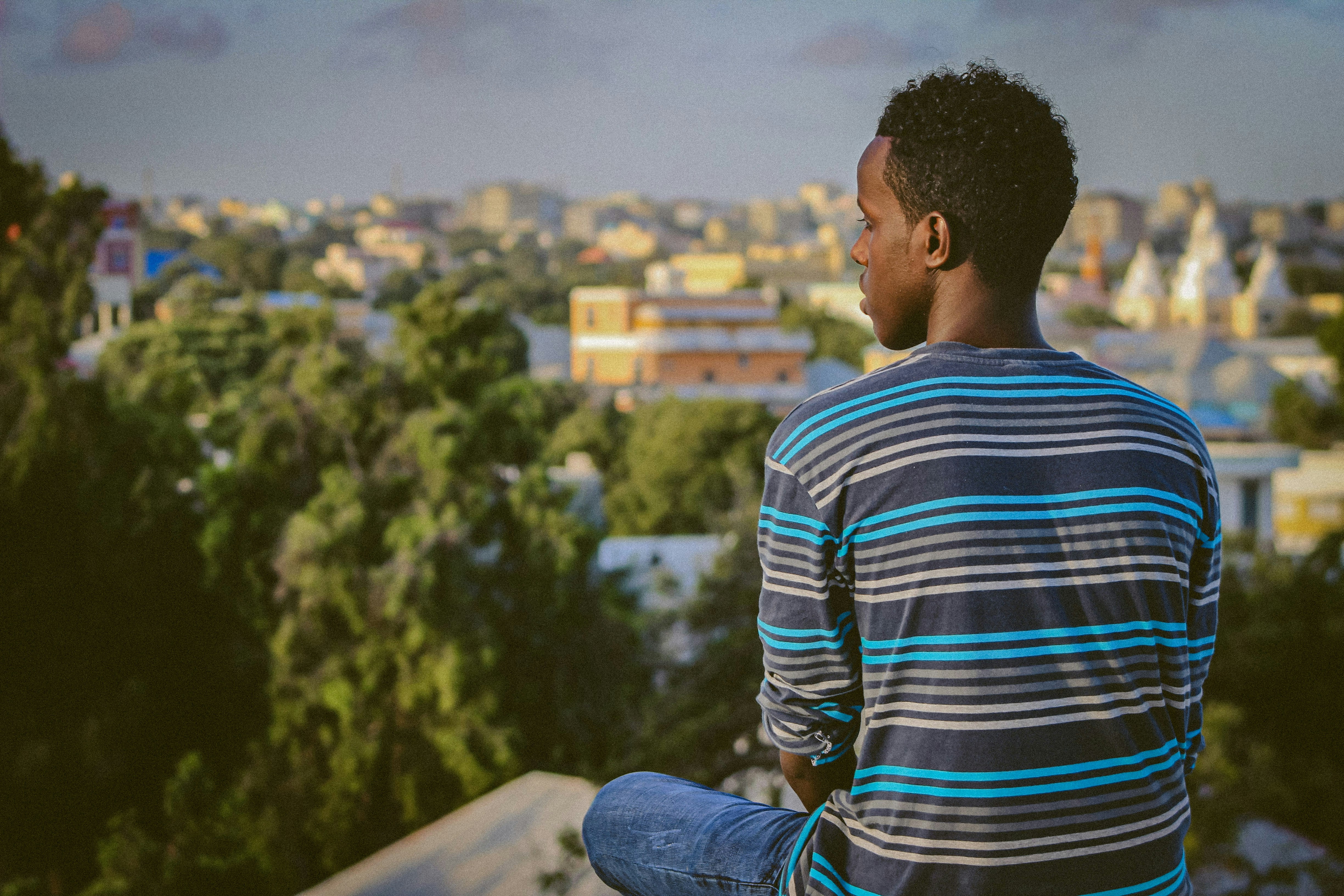 Person gazing over a vibrant cityscape with lush greenery and colorful buildings under a calm sky.