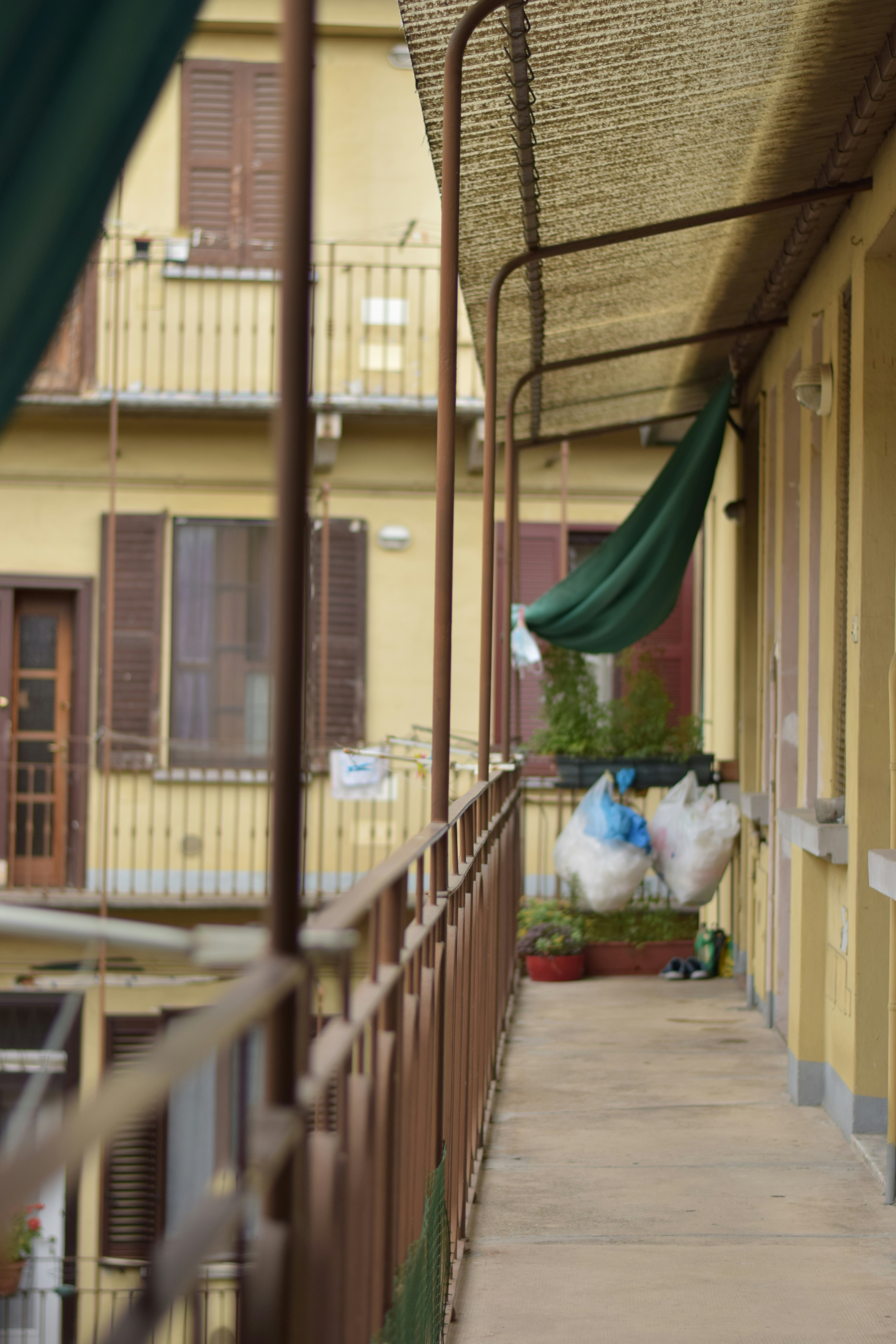 A narrow corridor adorned with green fabric drapes, leading to an outdoor space filled with potted plants and bags, reflecting a slice of urban living.